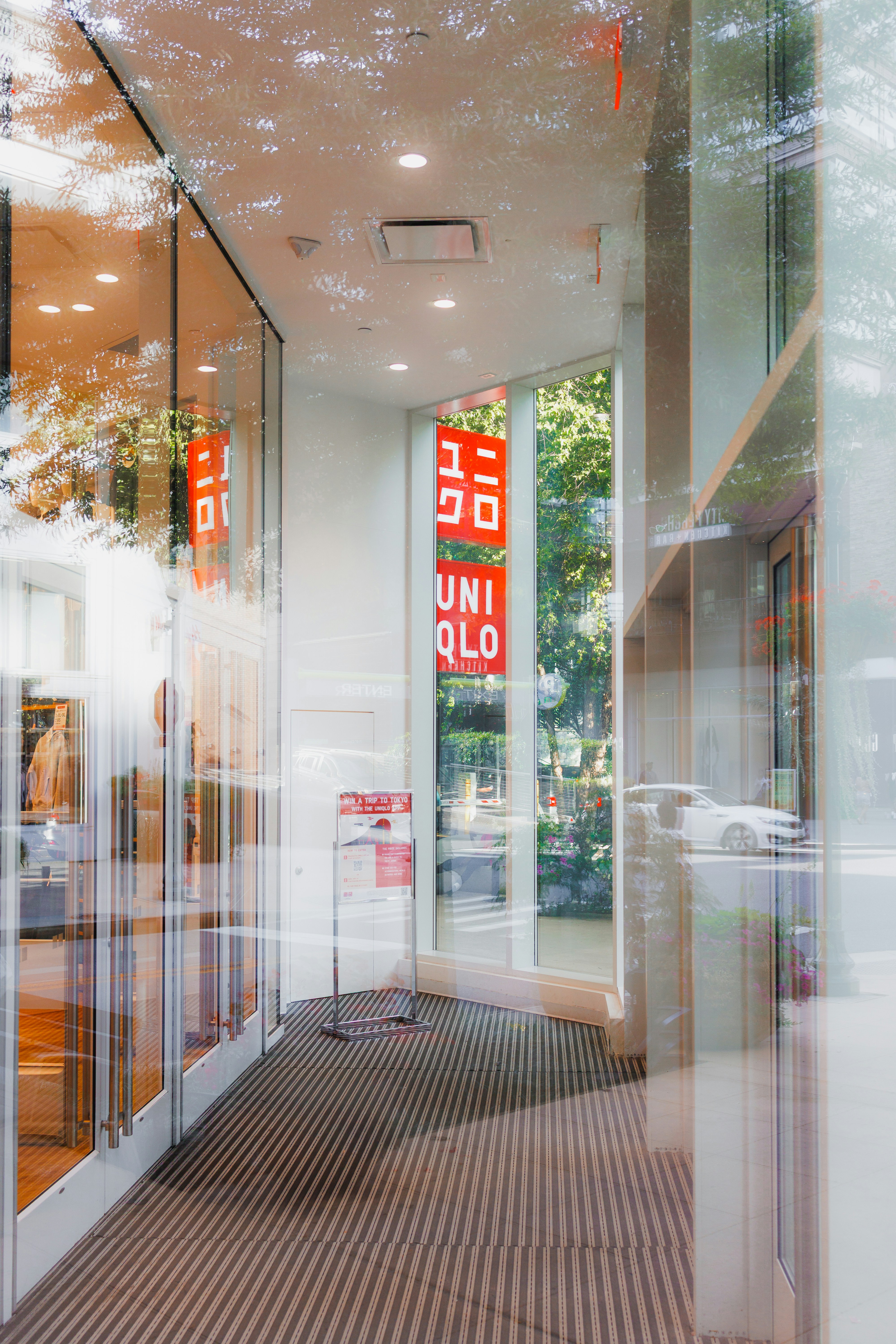 Uniqlo store entrance with reflections of trees and sky.