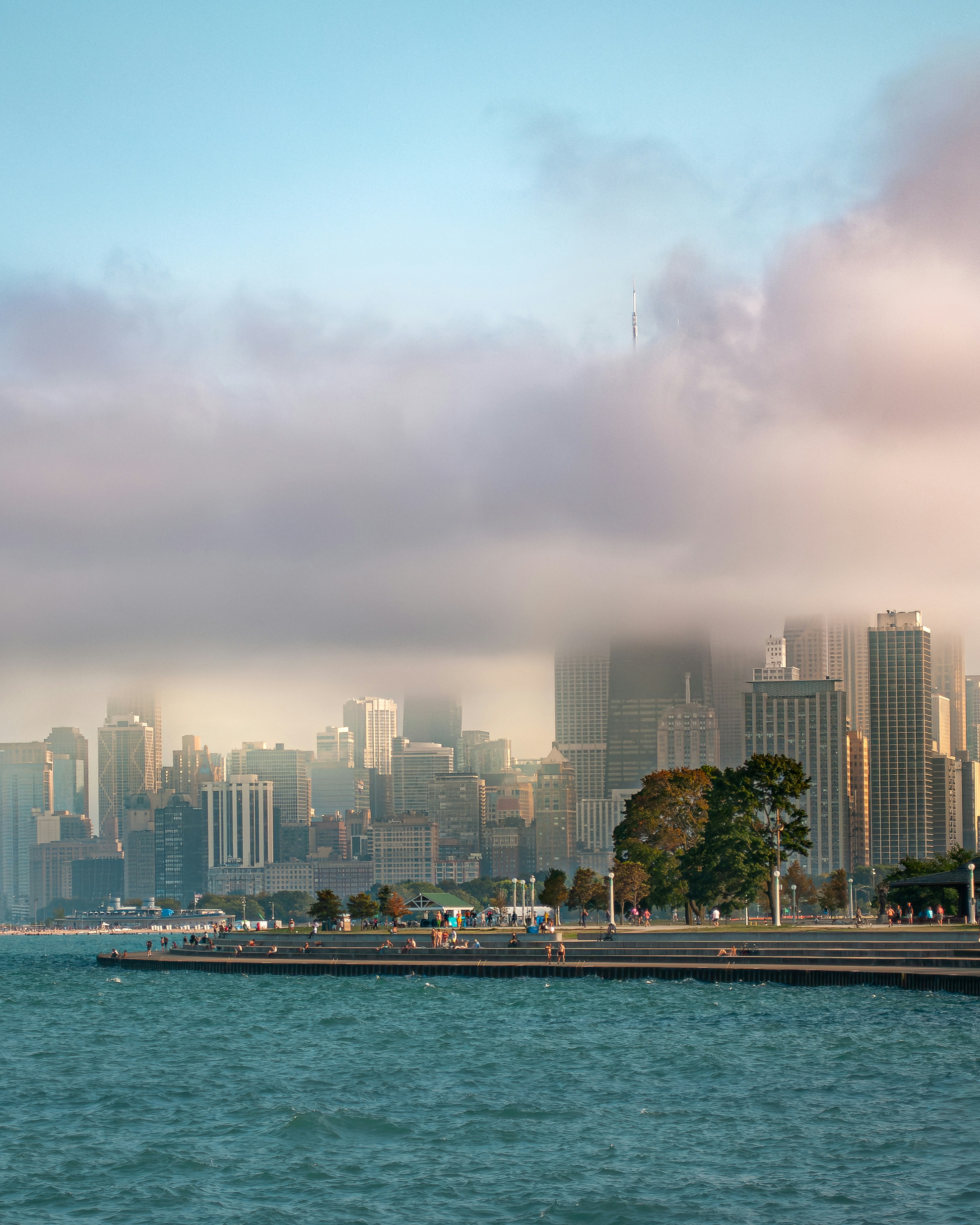 Chicago skyline fades in clouds while sunlight filters through the haze | City skyline emerges from morning fog over water.