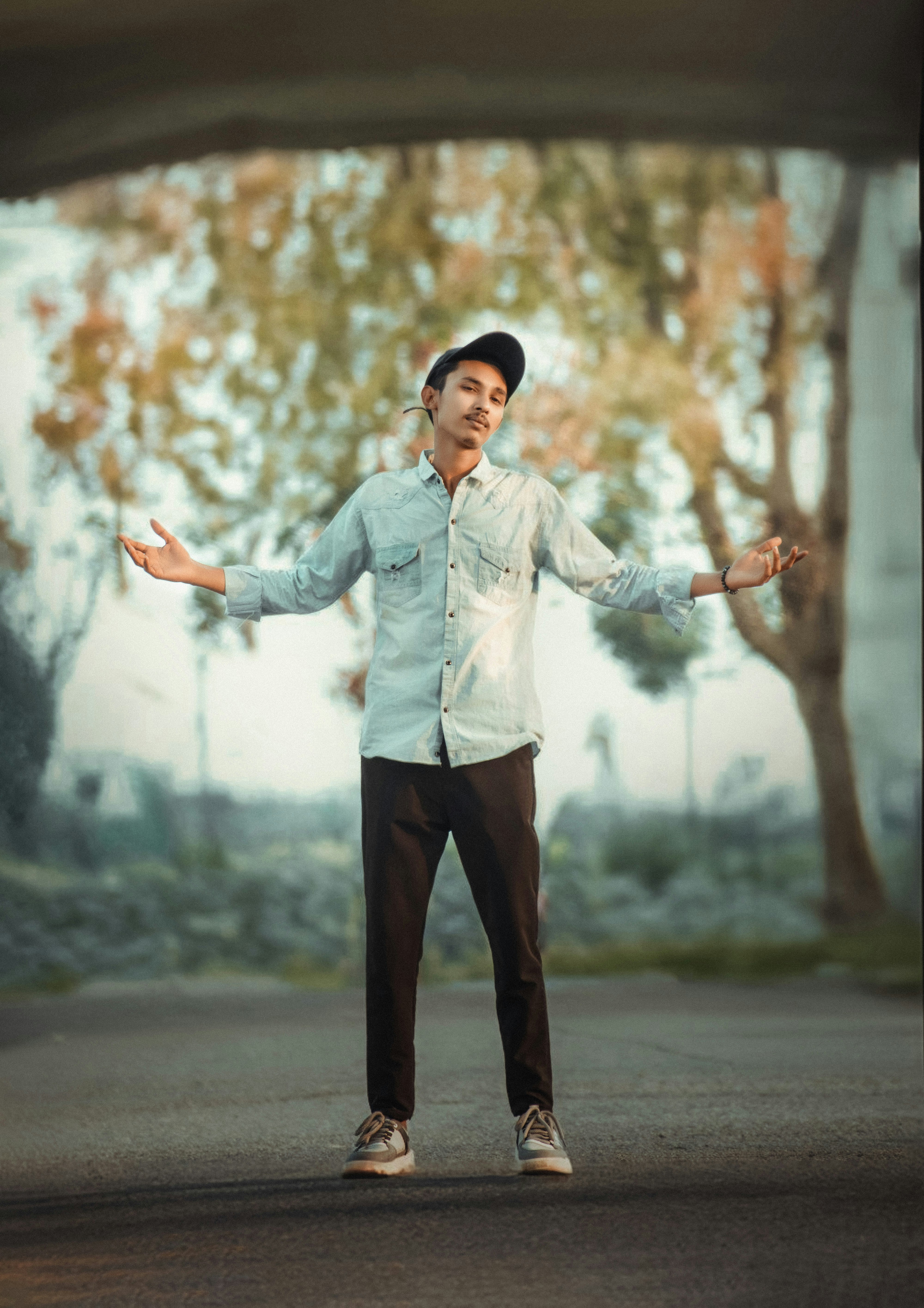 A young man stands with arms outstretched outdoors.