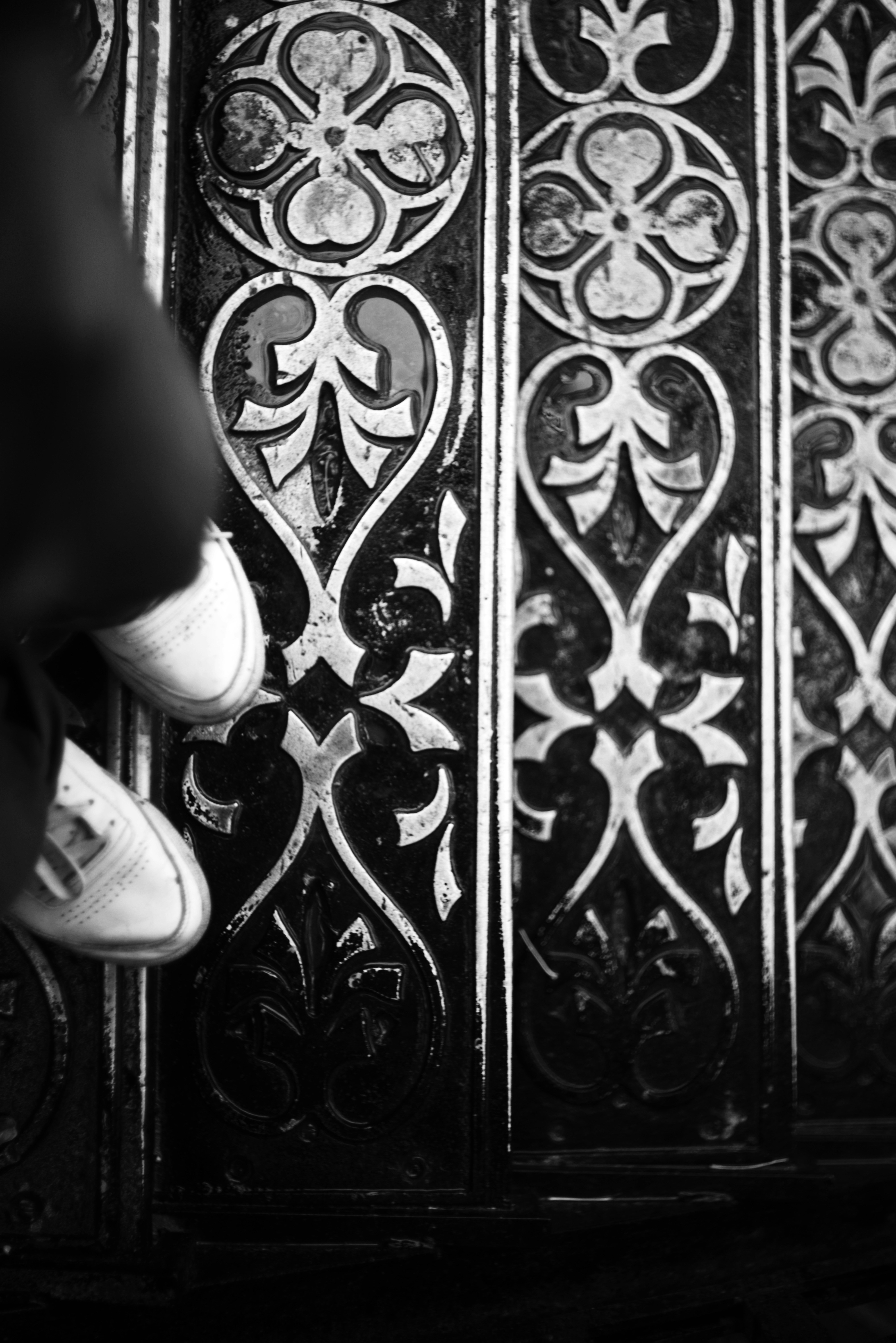 Close-up of ornate flooring with a pair of sneakers, highlighting the intricate patterns in monochrome tones.
