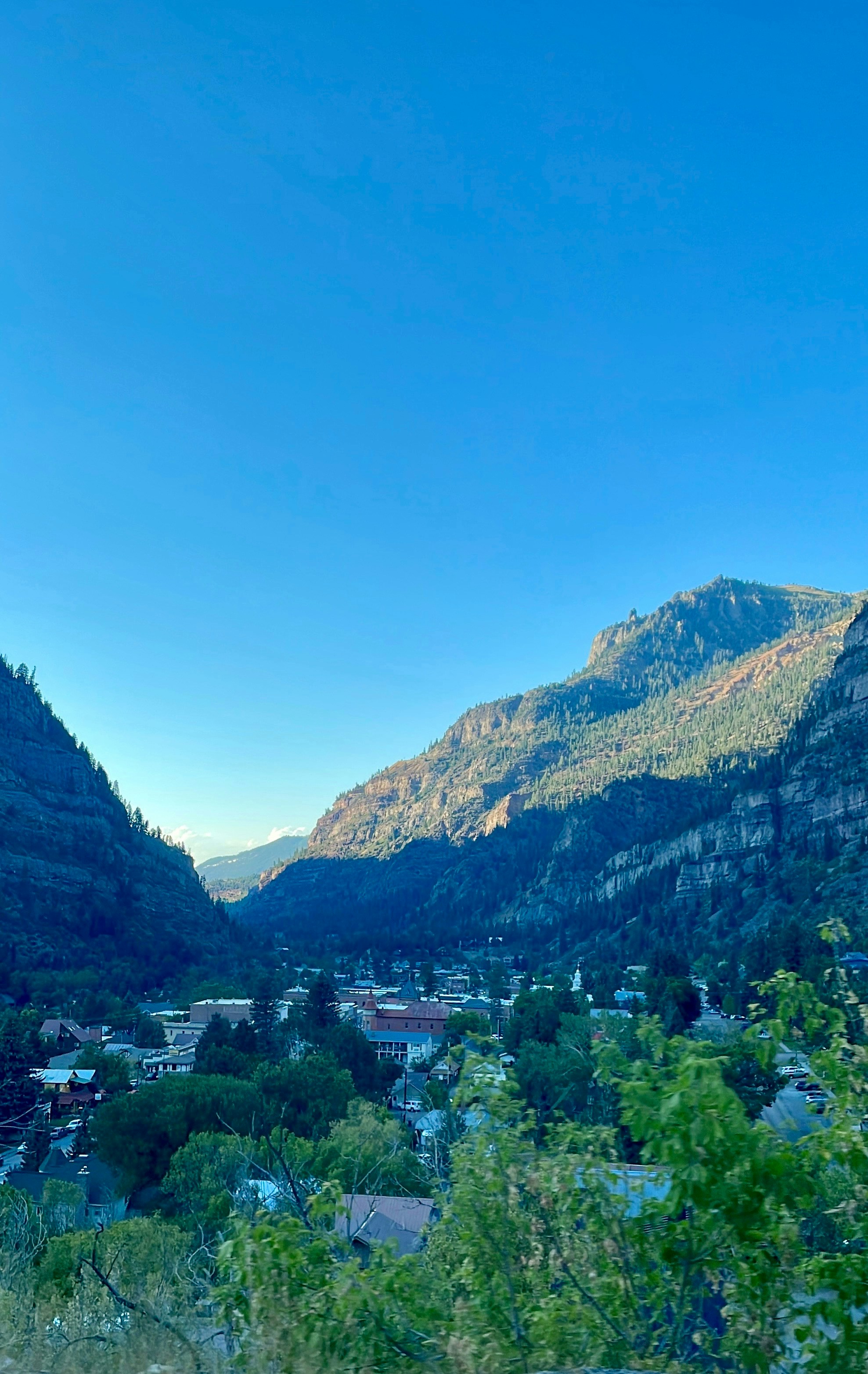 Valley town nestled between sunlit mountains under clear sky.