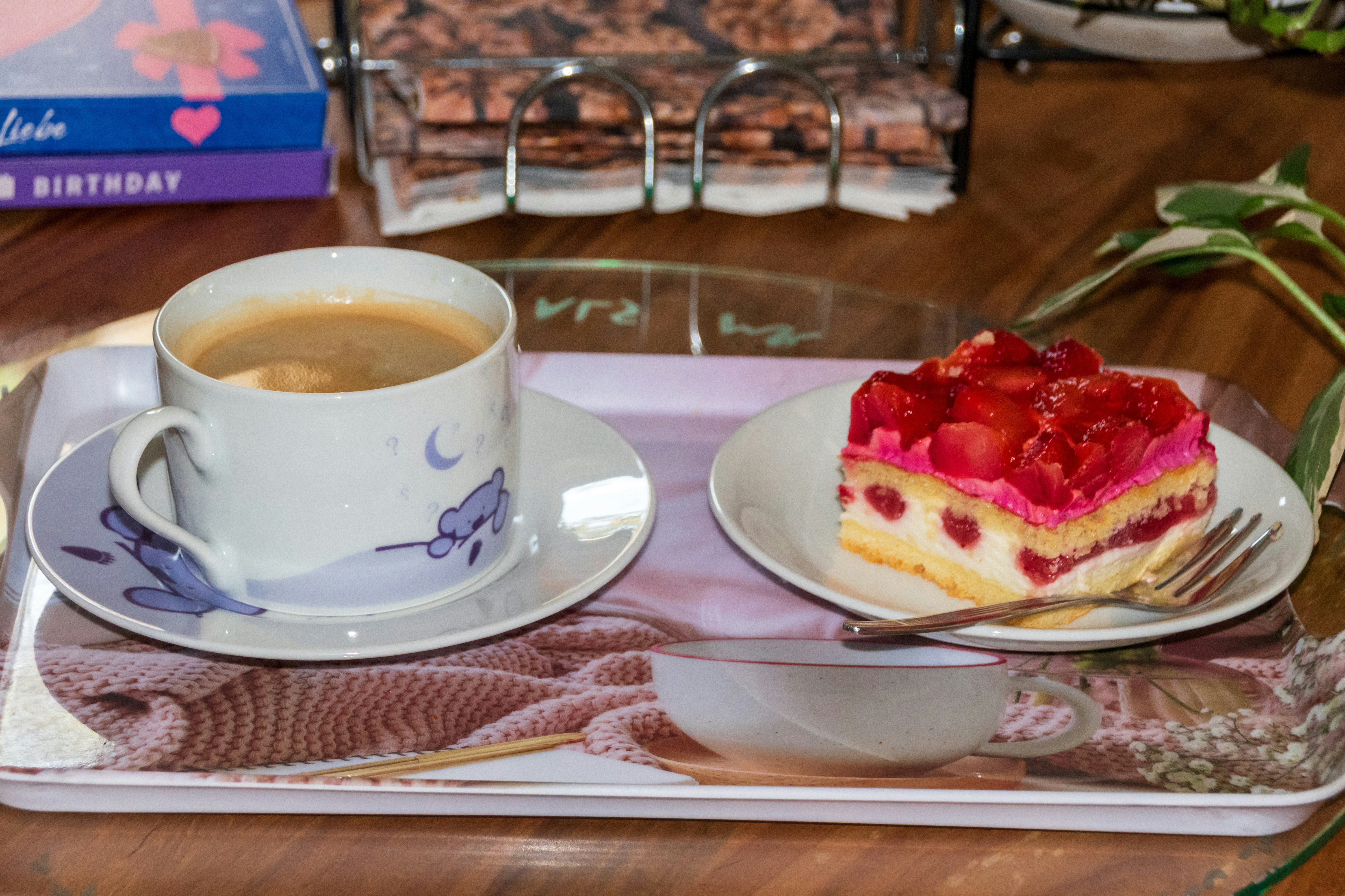 A cup of coffee beside a slice of strawberry cake on a decorative tray, showcasing a cozy moment of indulgence.