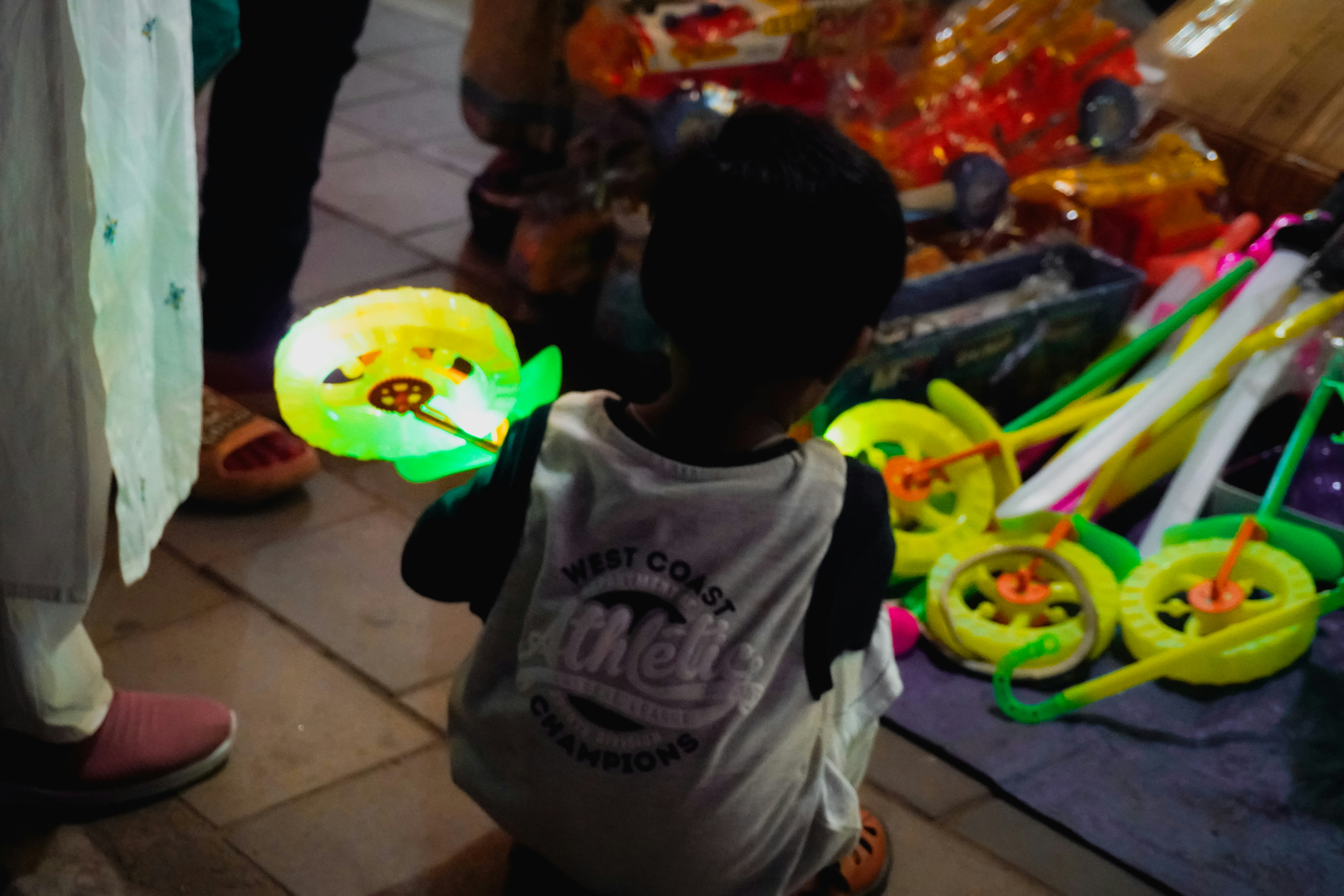 Back-Turned Wonder Amid Neon Toy Wheels at a Street Market