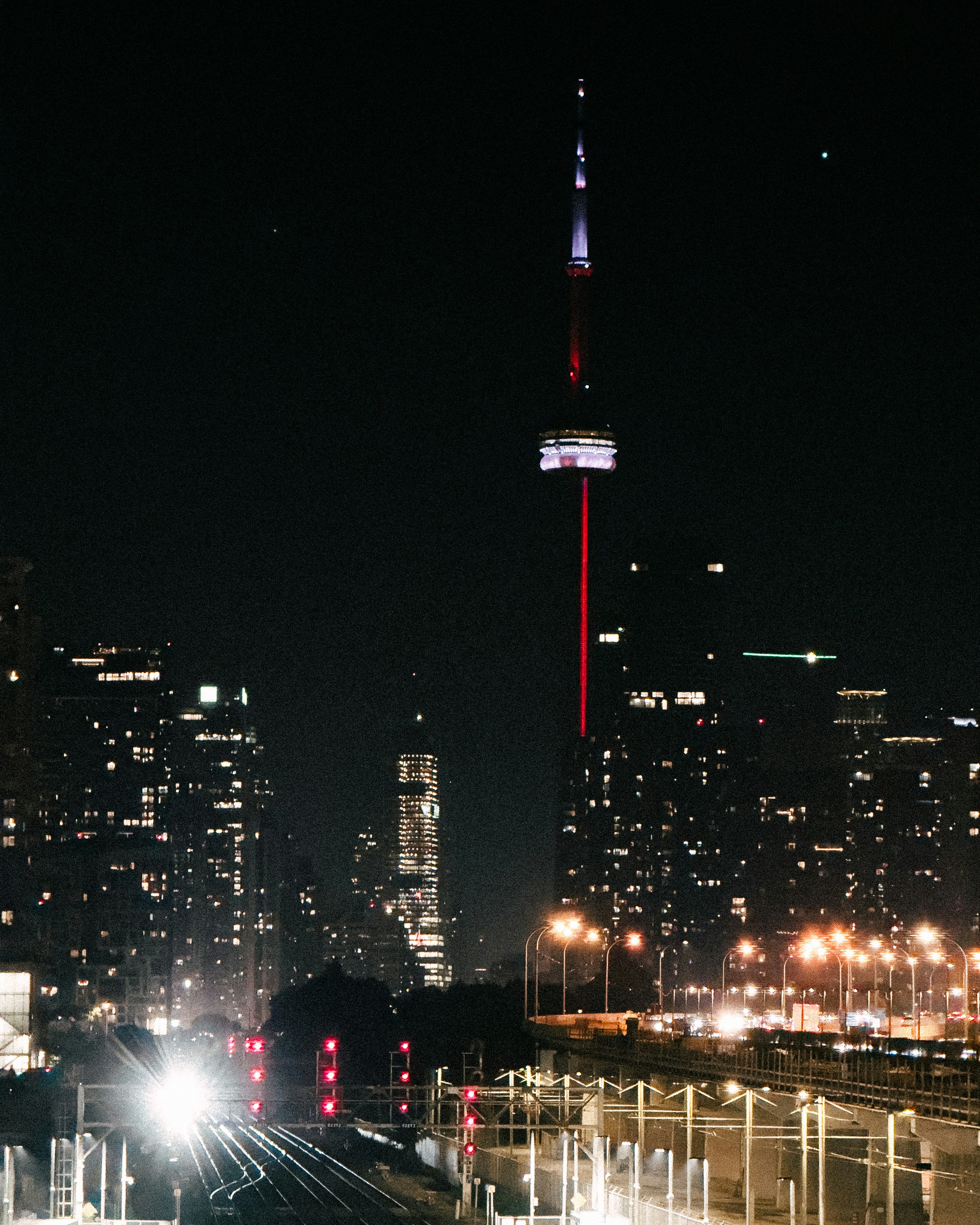 Cityscape at night with illuminated tower and train tracks.