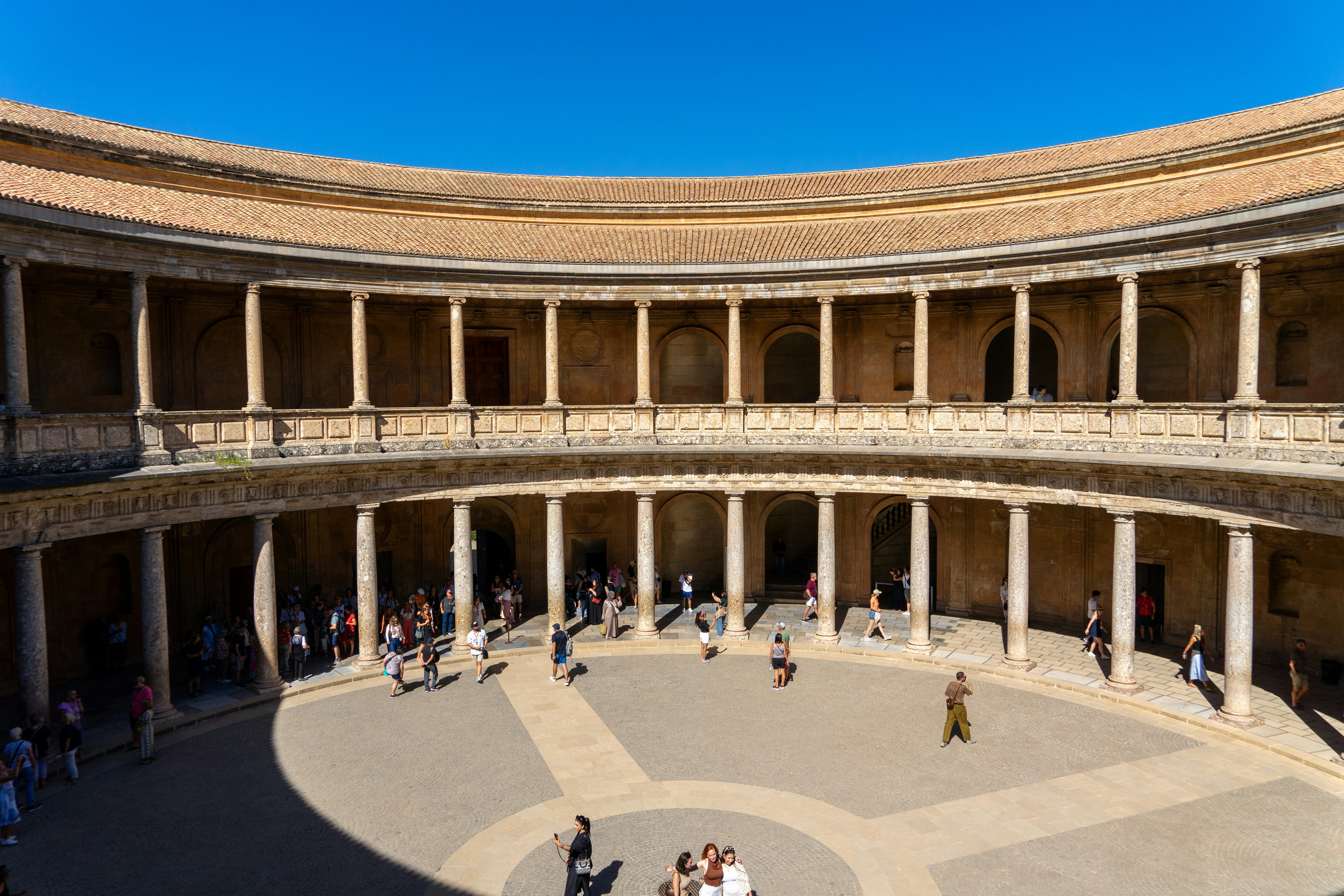 A vibrant courtyard surrounded by classical columns, filled with visitors exploring the historic architecture under a clear blue sky.