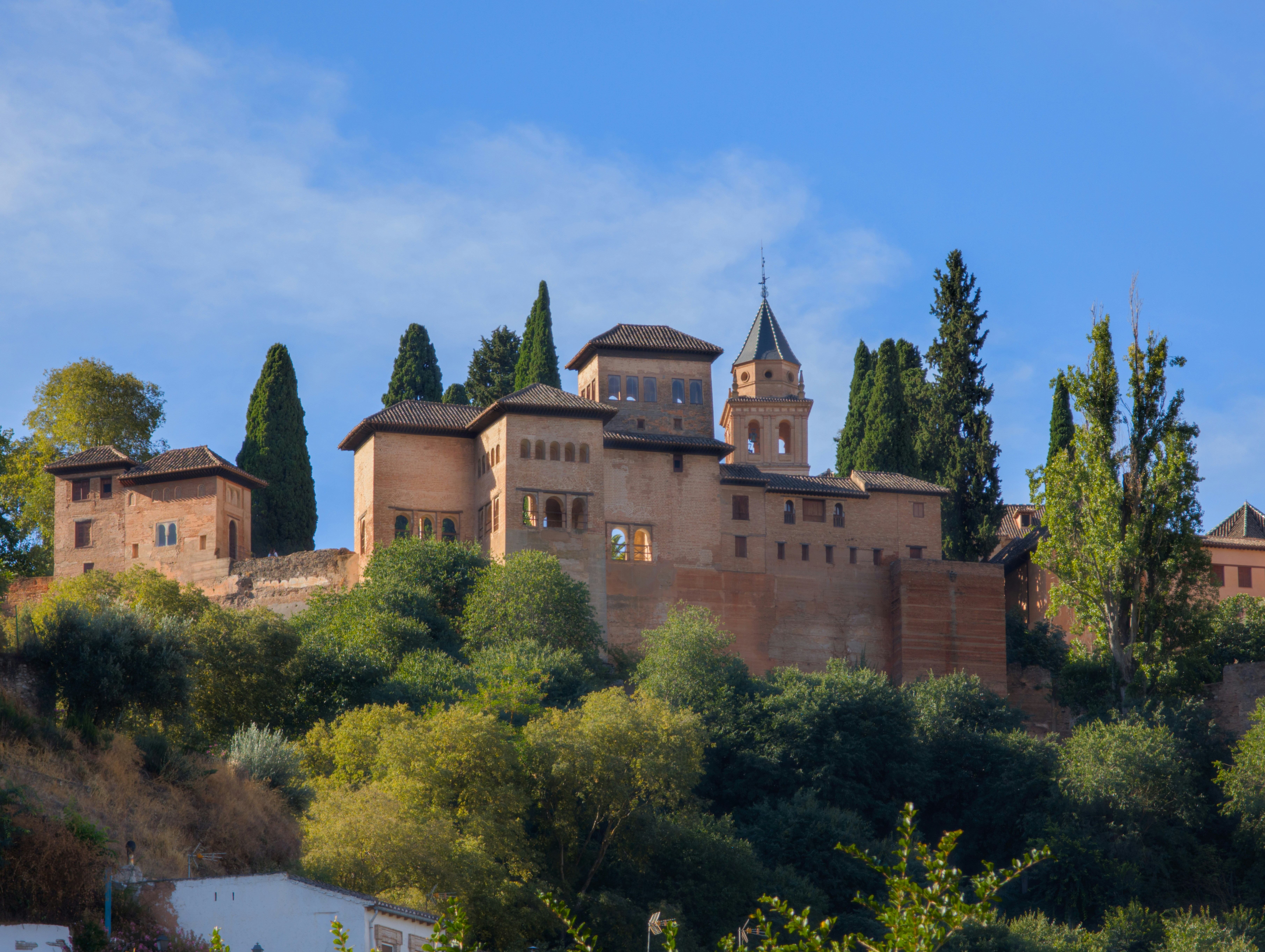 The Alhambra fortress rises elegantly amidst lush greenery, showcasing its intricate architecture against a clear blue sky.