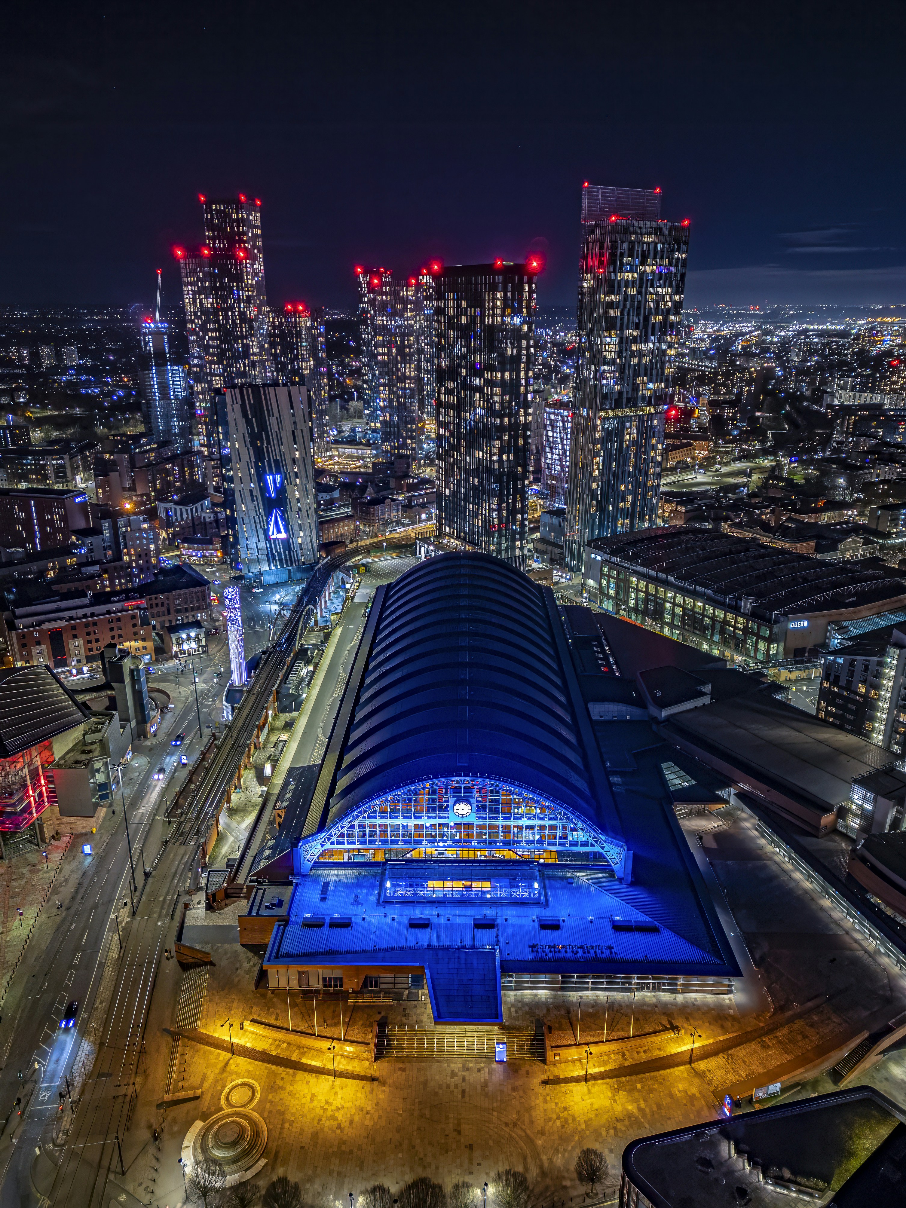 Cityscape at night with illuminated train station and skyscrapers.