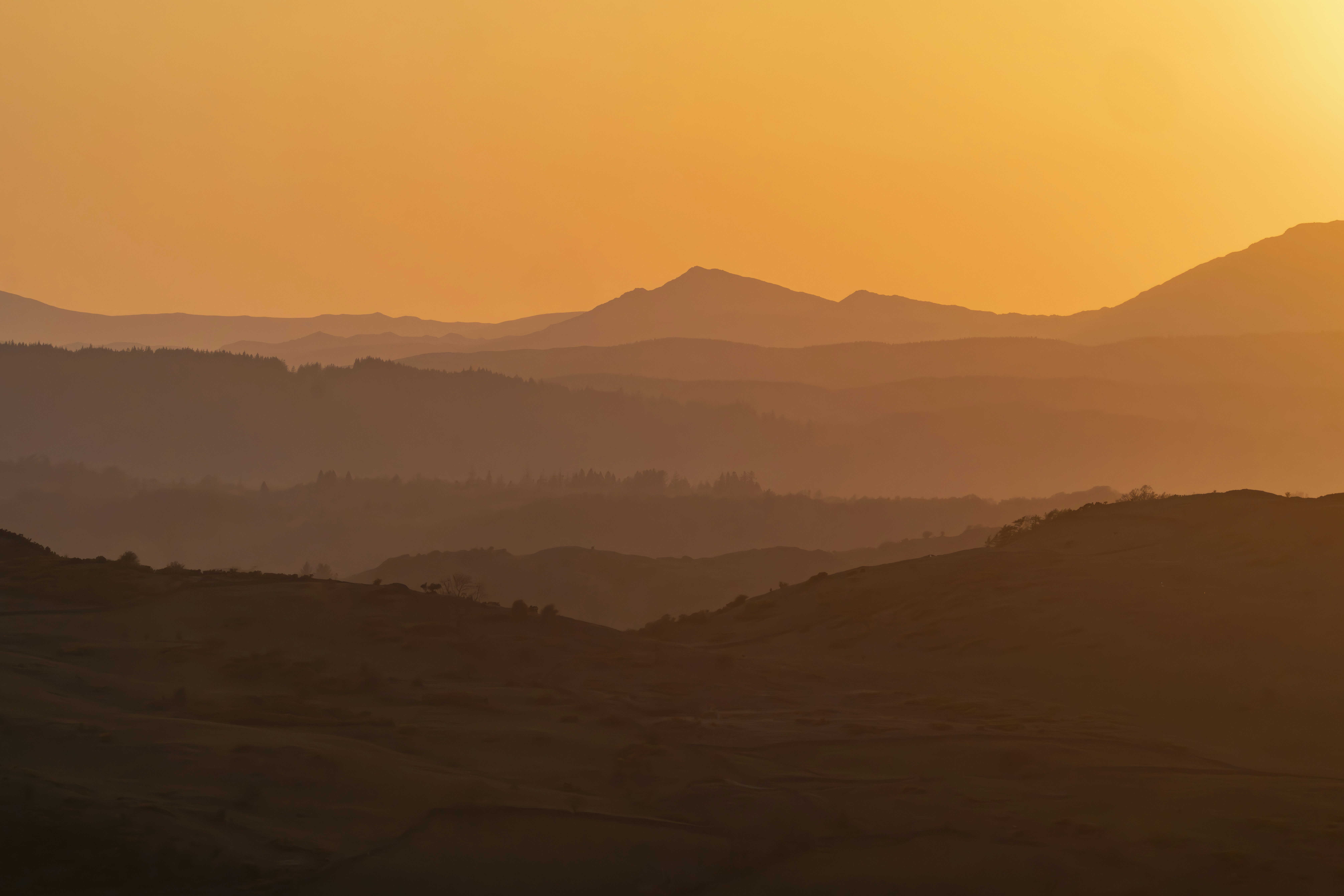 Hazy mountain layers at sunset with orange sky