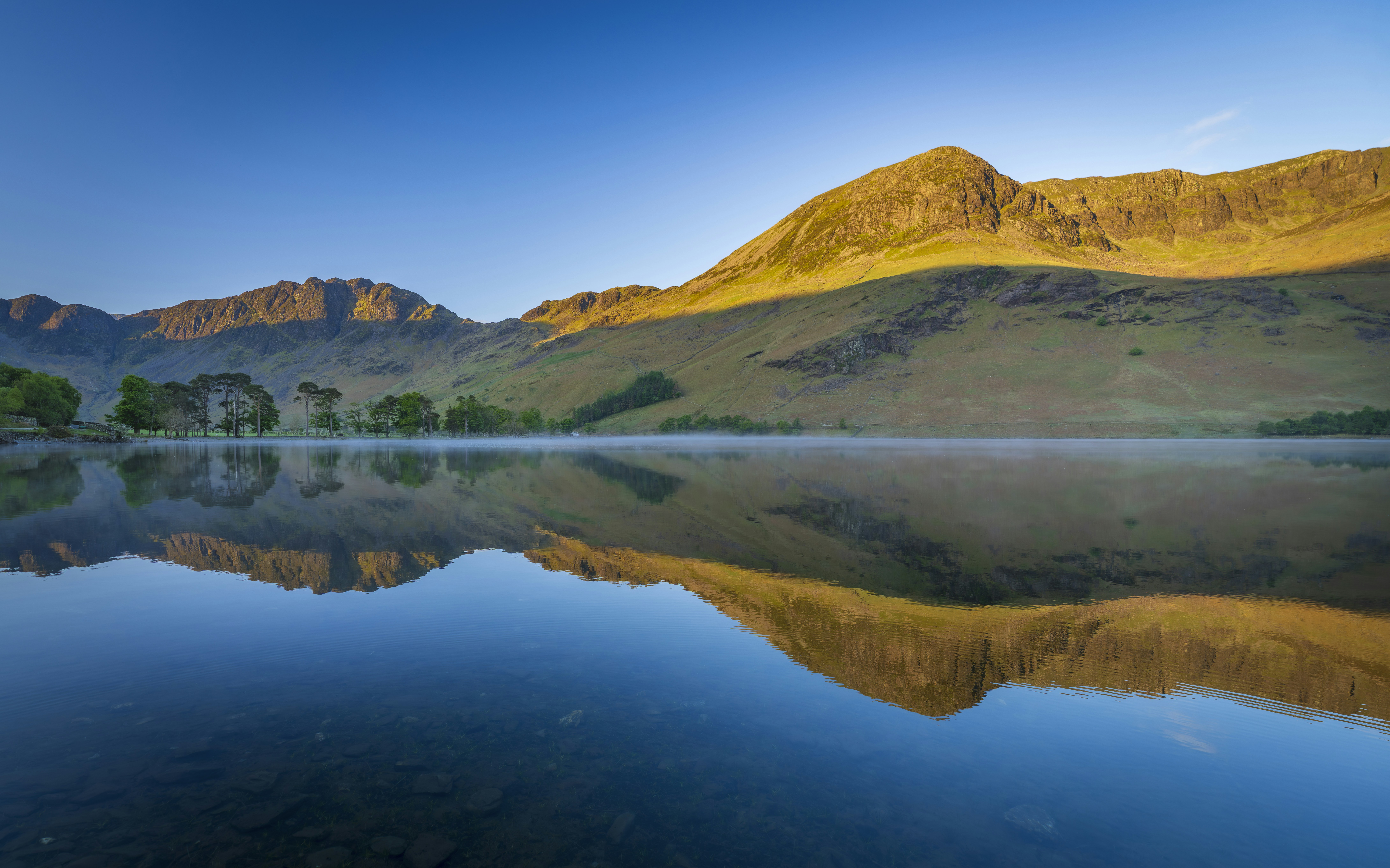 Golden mountain peaks reflected in a calm lake at sunrise.