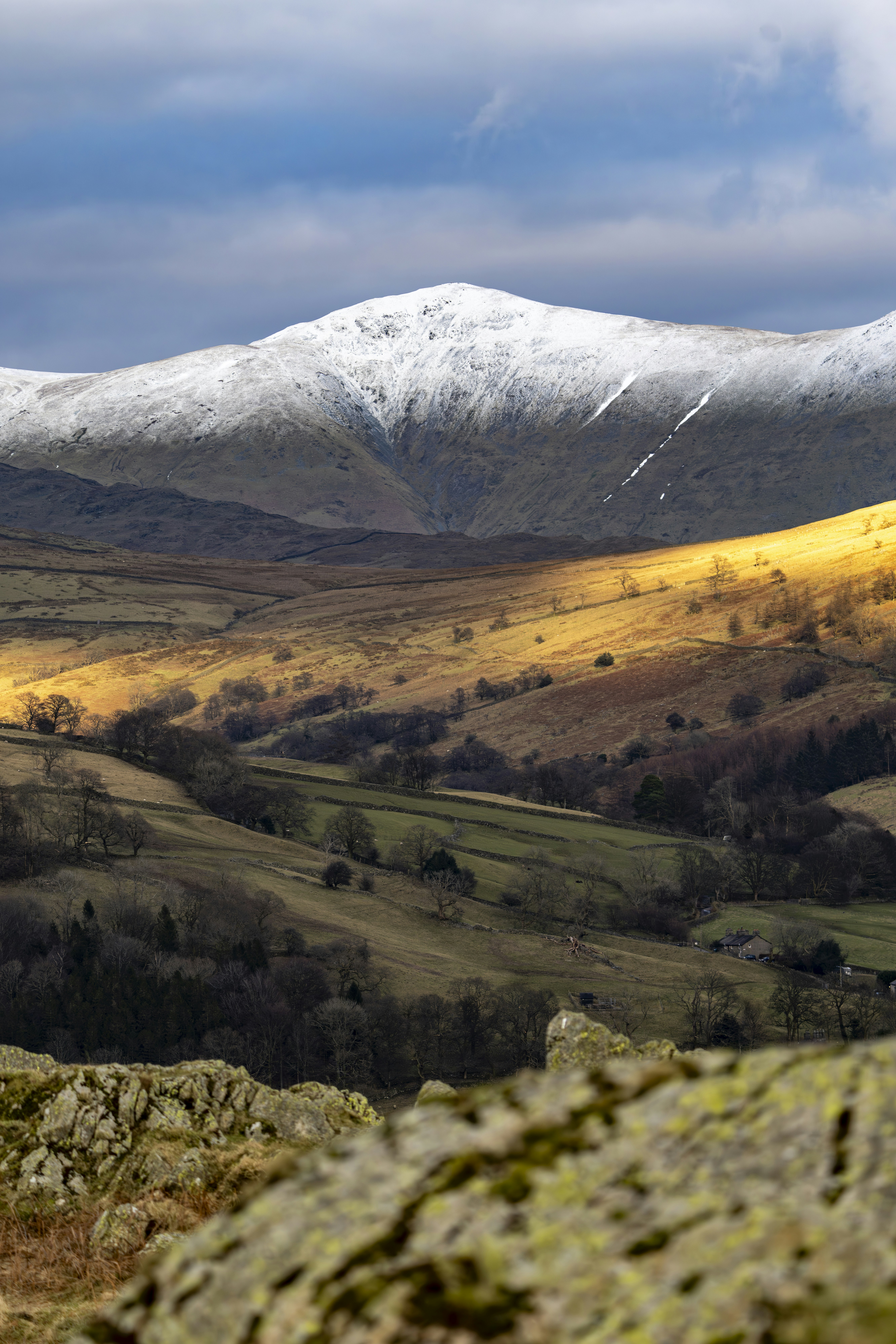 Sunlight illuminates snow-capped mountains and rolling hills.