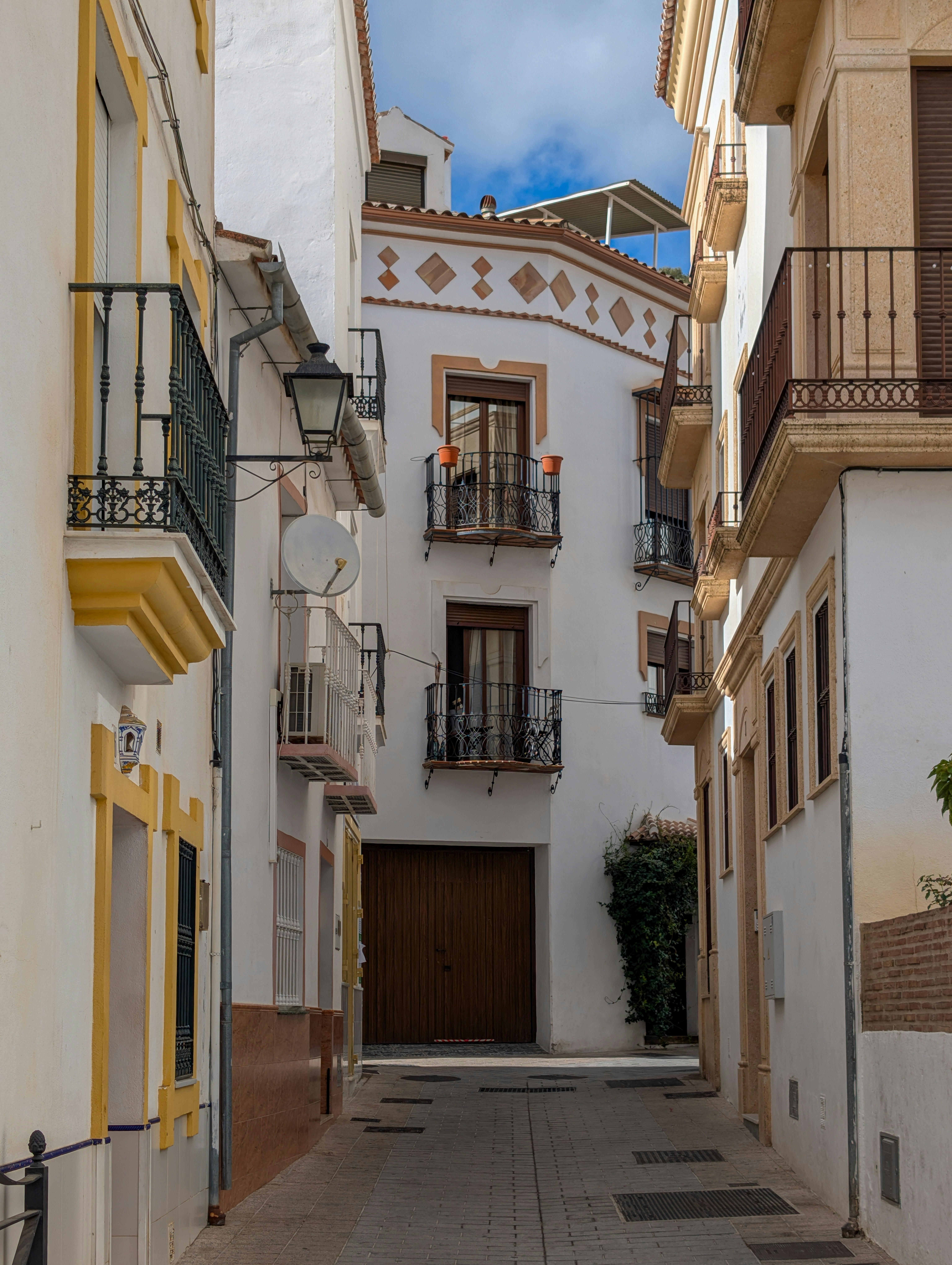 Narrow street between white buildings with balconies.