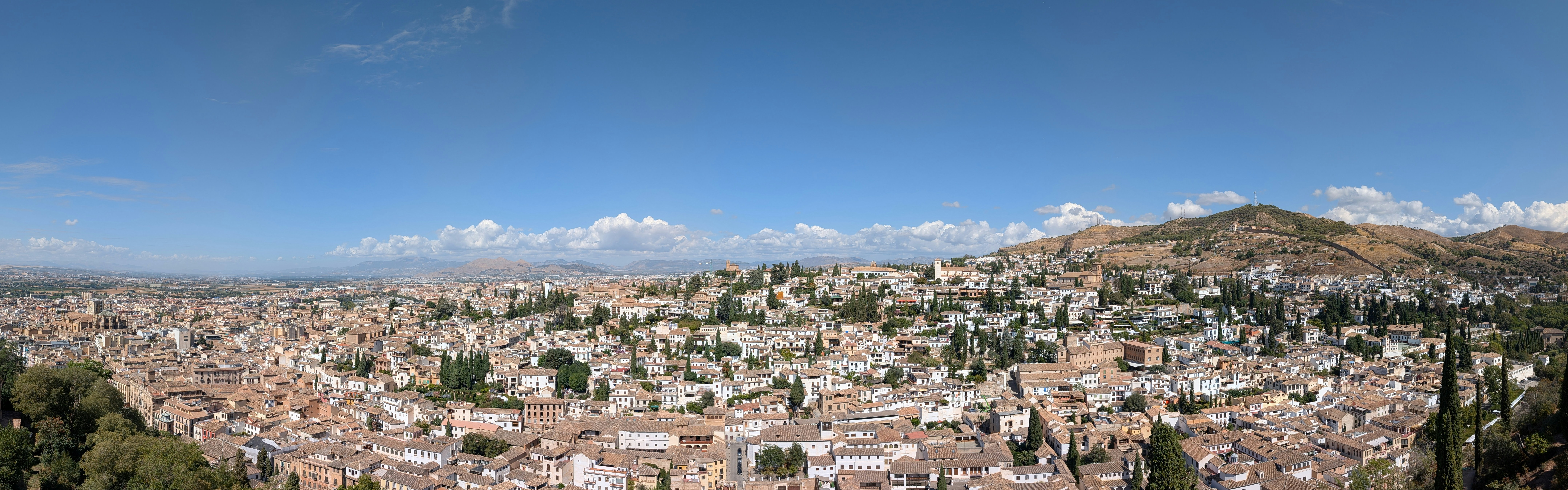 Panoramic view of Granada showcasing its terracotta rooftops and surrounding hills under a clear blue sky.