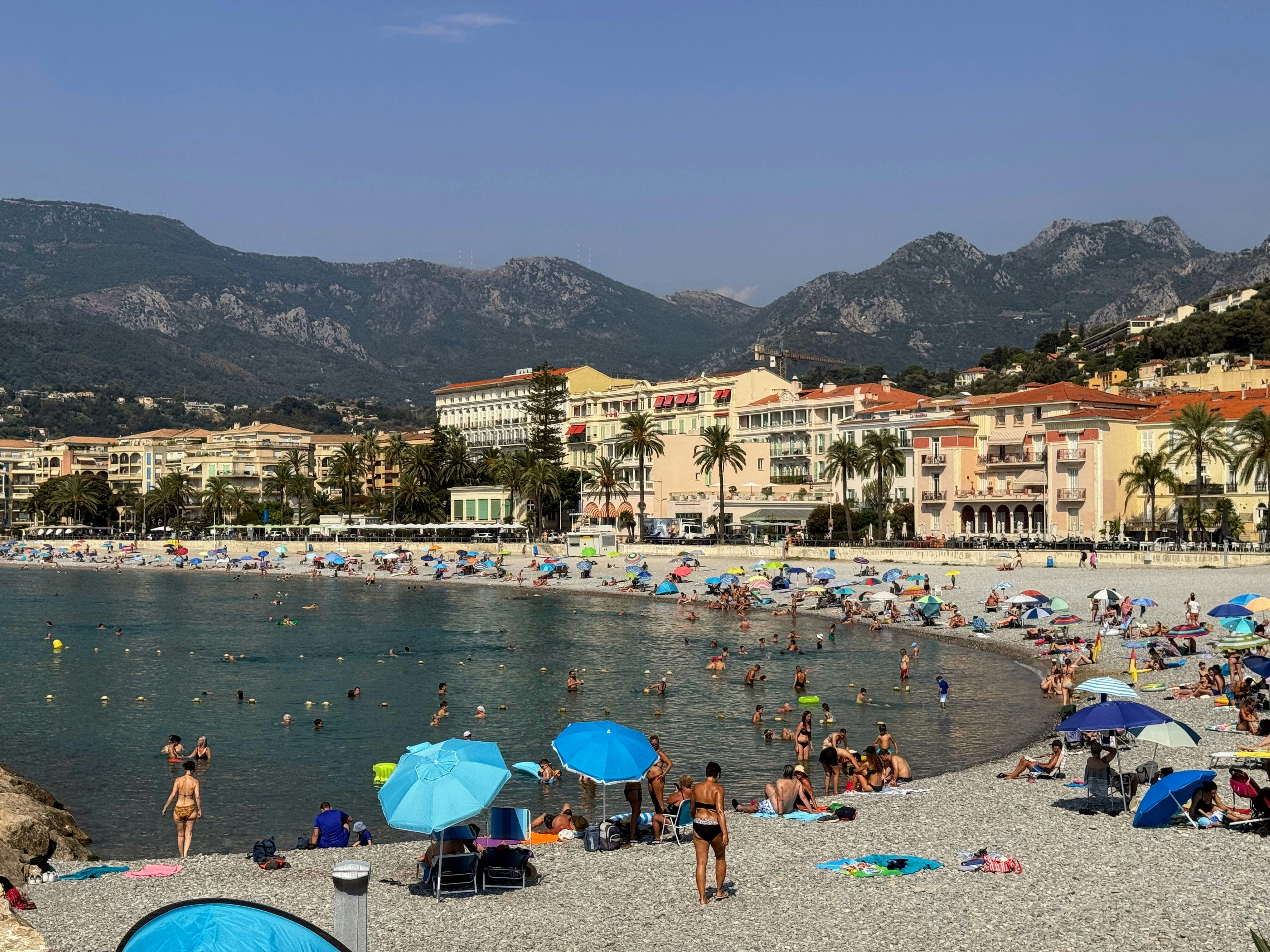 Crowded beach with colorful buildings and mountains in background