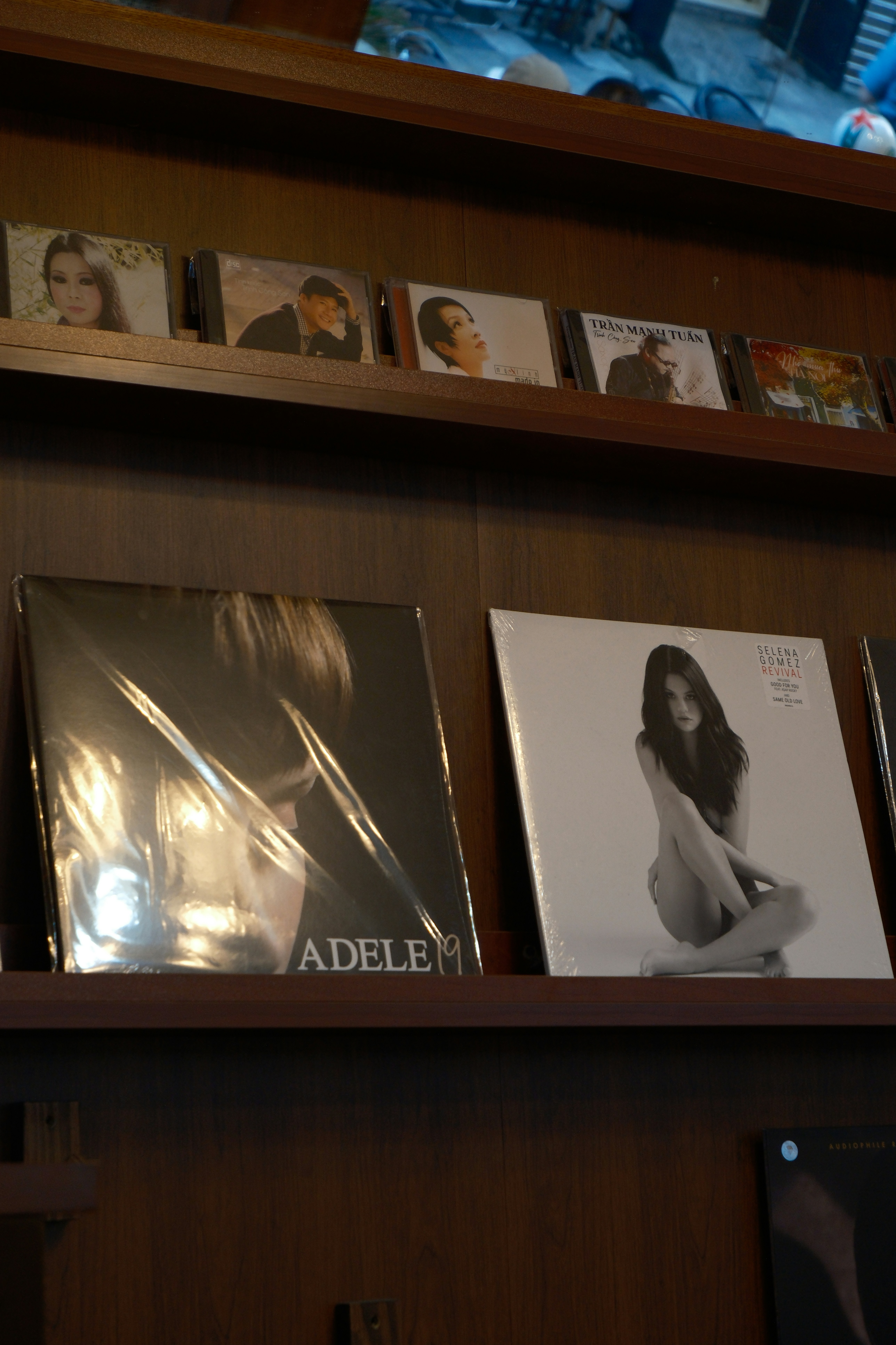 Vinyl records displayed on a wooden shelf, featuring album covers of Adele and other artists. The warm ambiance complements the nostalgic feel of the collection.