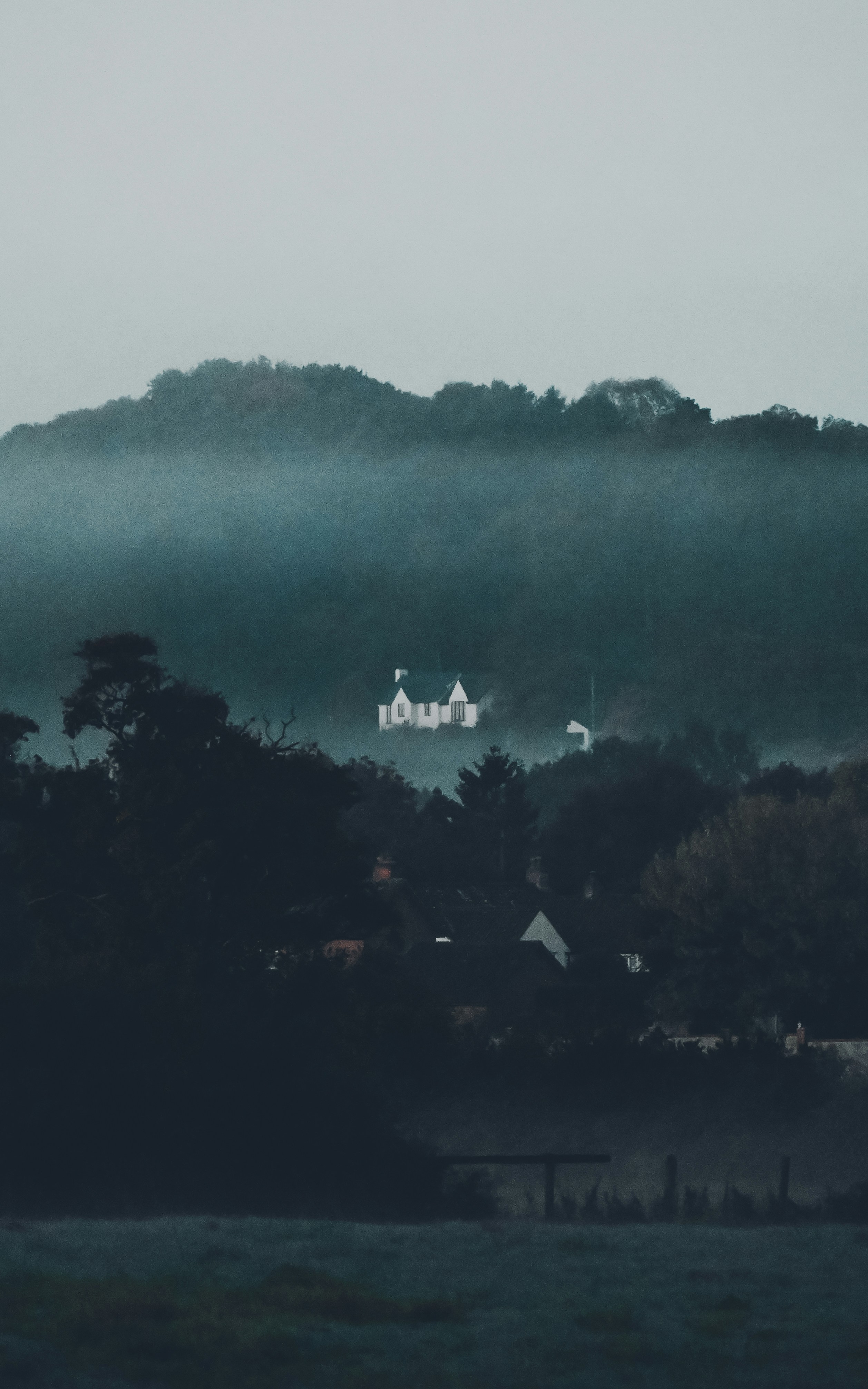 White house nestled in misty, tree-covered hills.