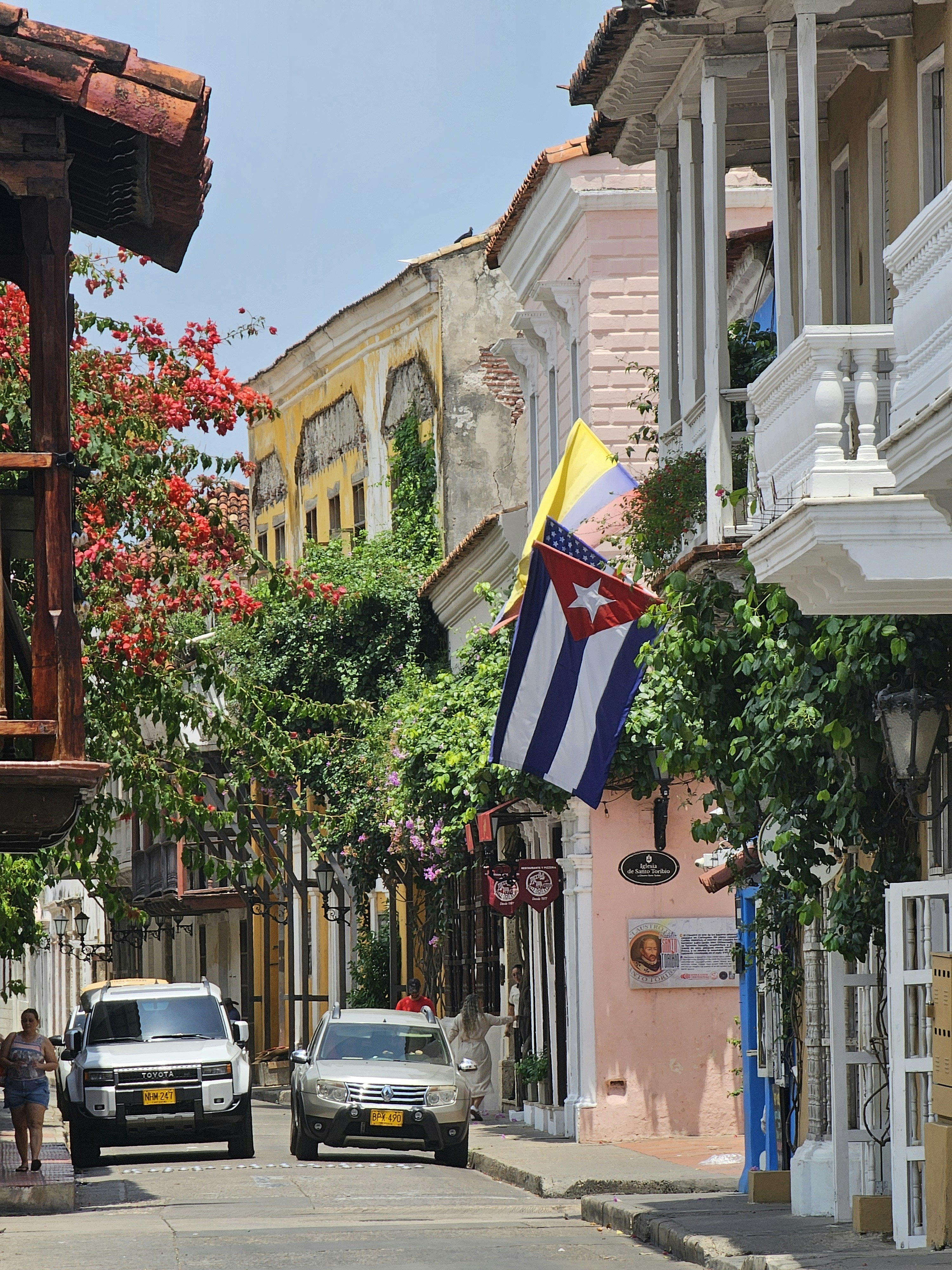 Cars drive down a narrow street with flags.