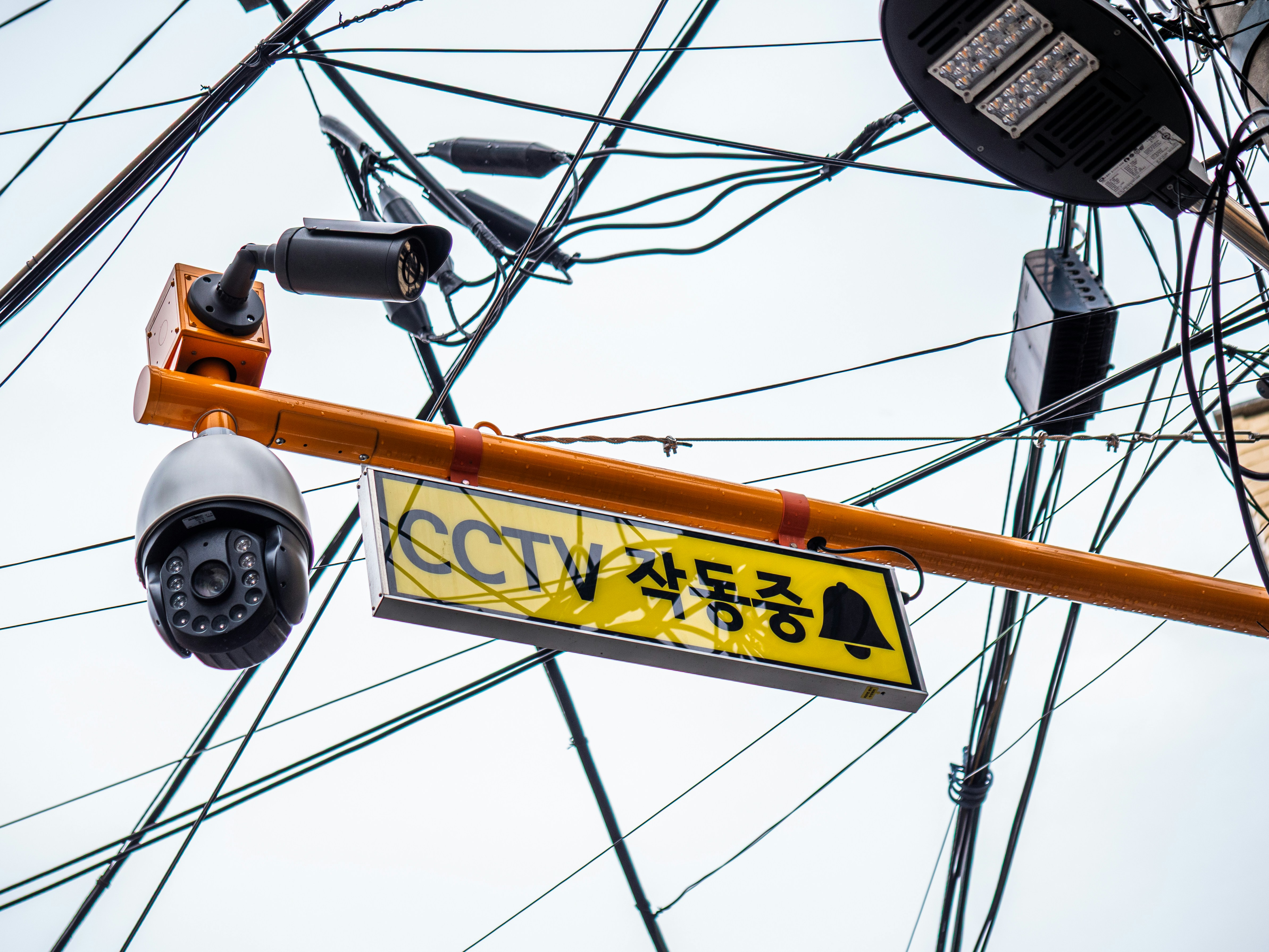 Cctv cameras and wires against a cloudy sky