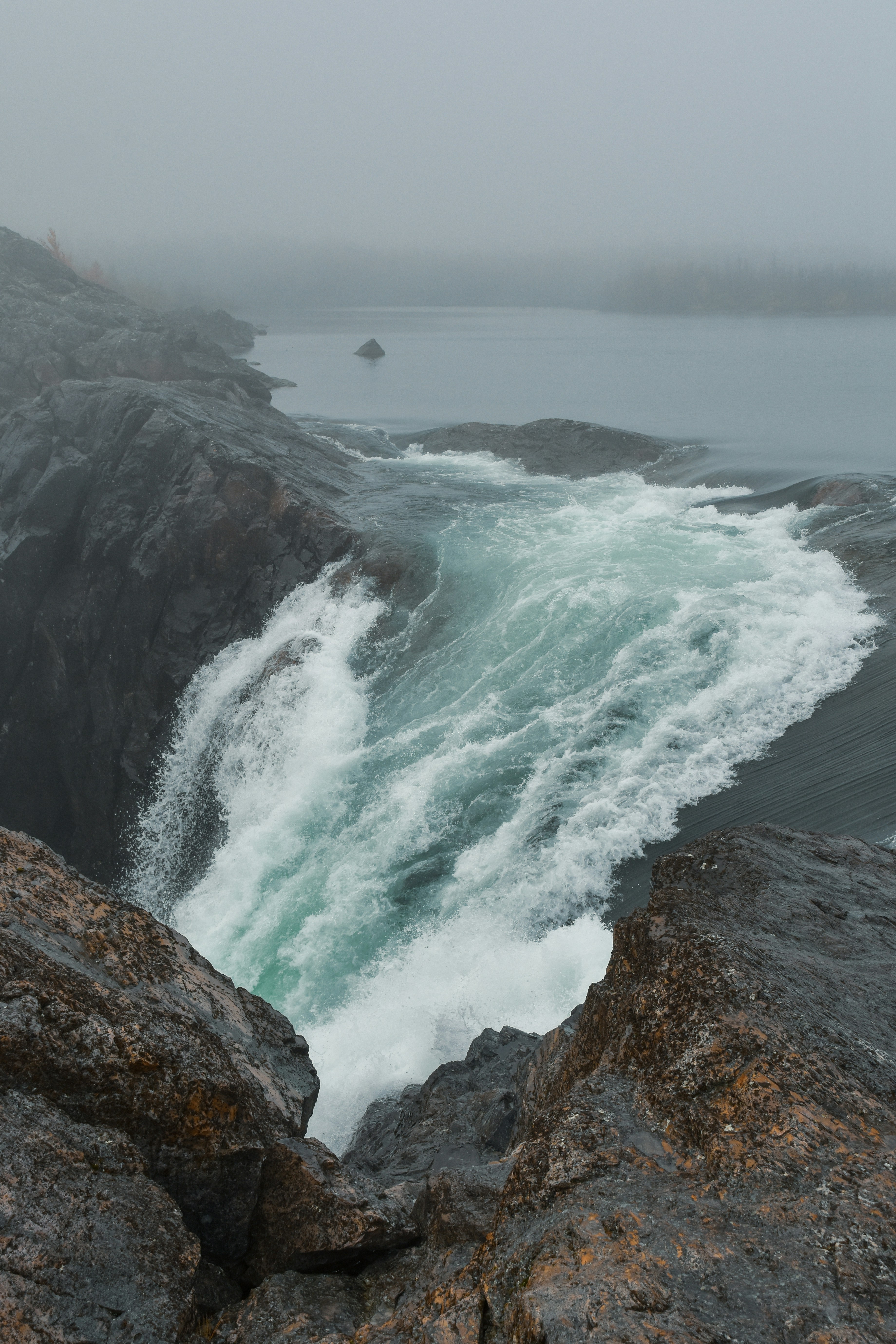 Teal Cascade Between Slate Rocks Under a Misty Coastal Horizon