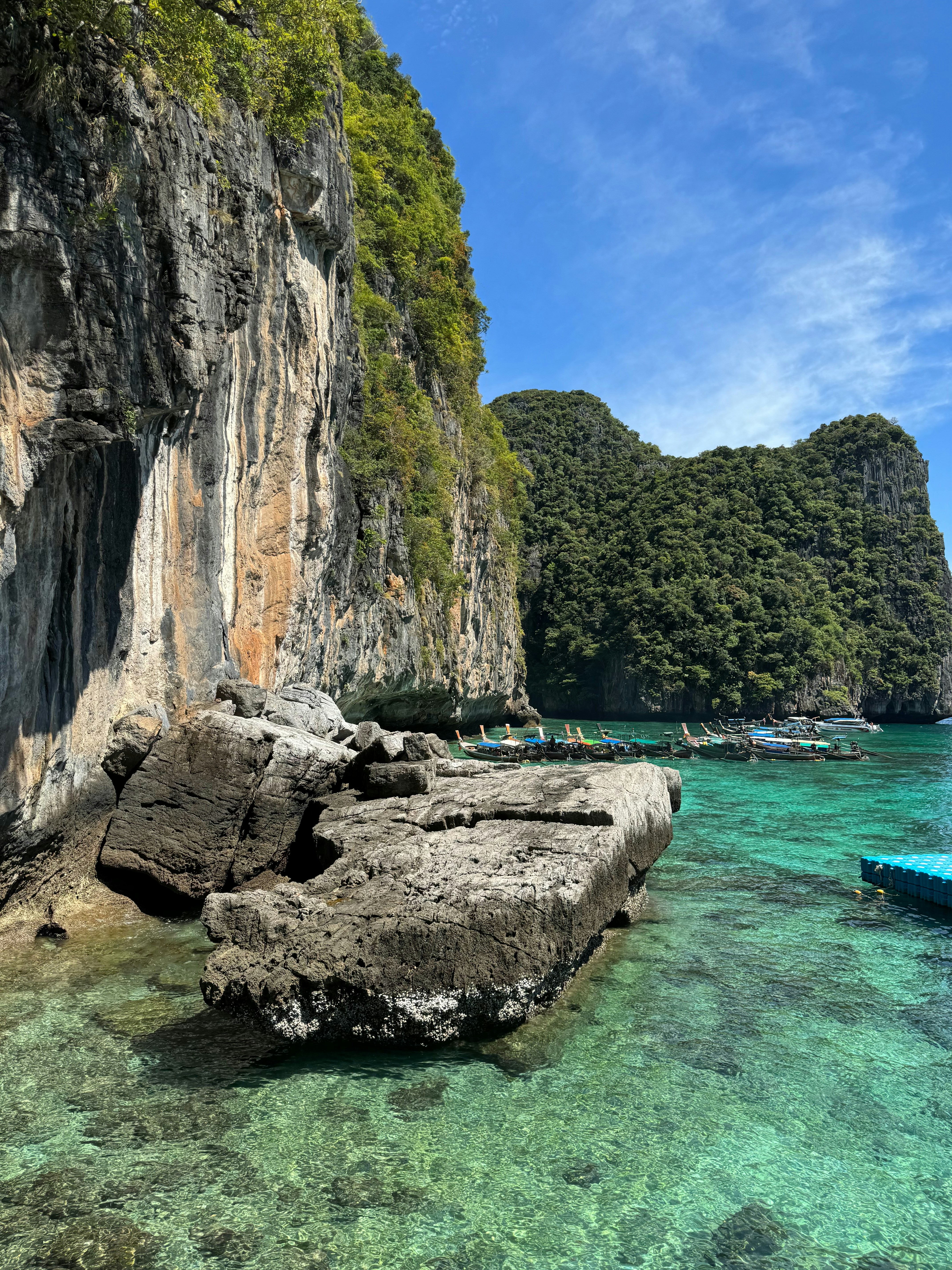 A stunning tropical paradise on Phi Phi Island with turquoise waters, limestone cliffs, and lush greenery, capturing the serene beauty of island life and vibrant natural scenery. | Limestone cliffs rise from turquoise waters with boats.