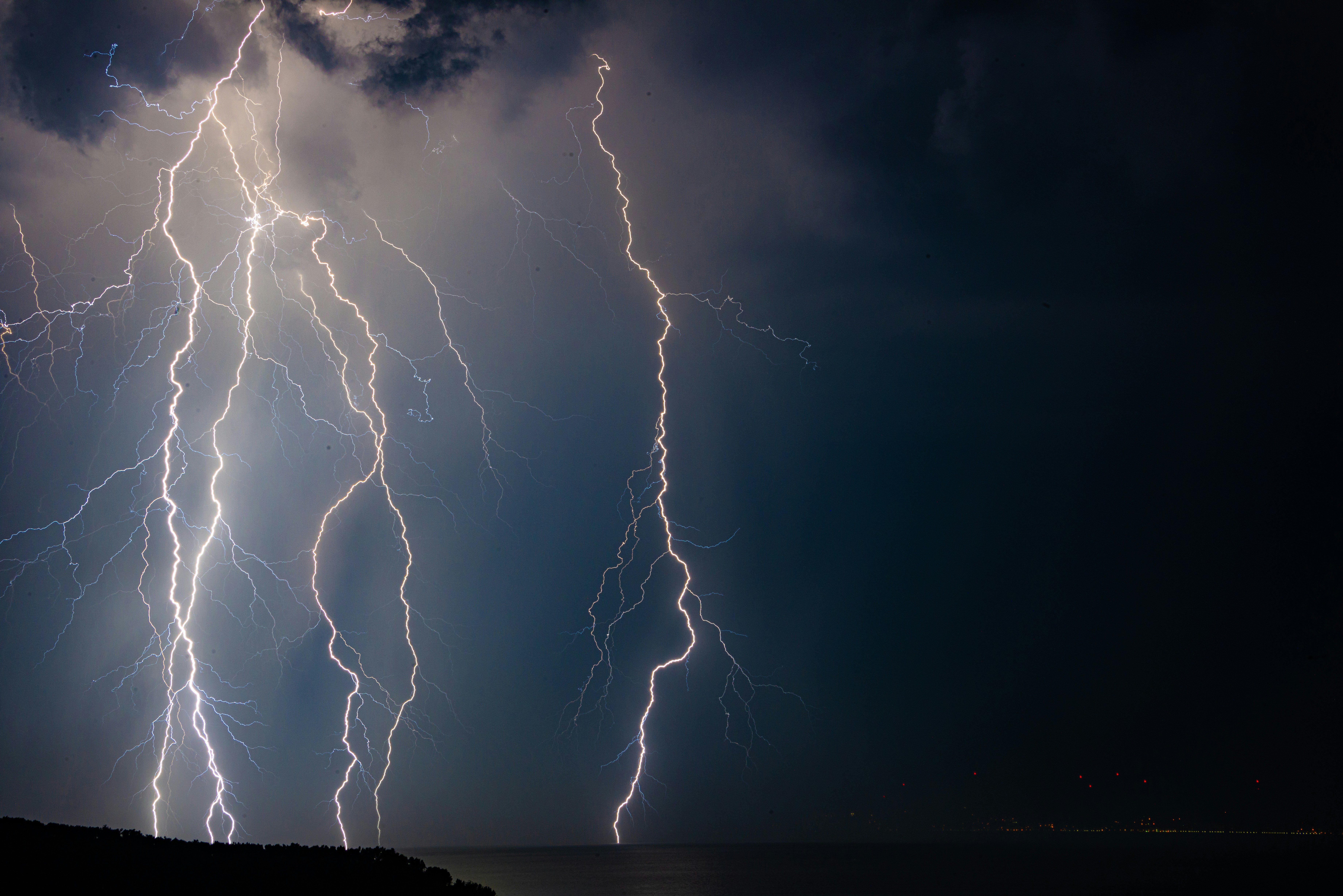 Lightning bolts descending from the sky | Multiple lightning strikes illuminate the dark night sky over water.