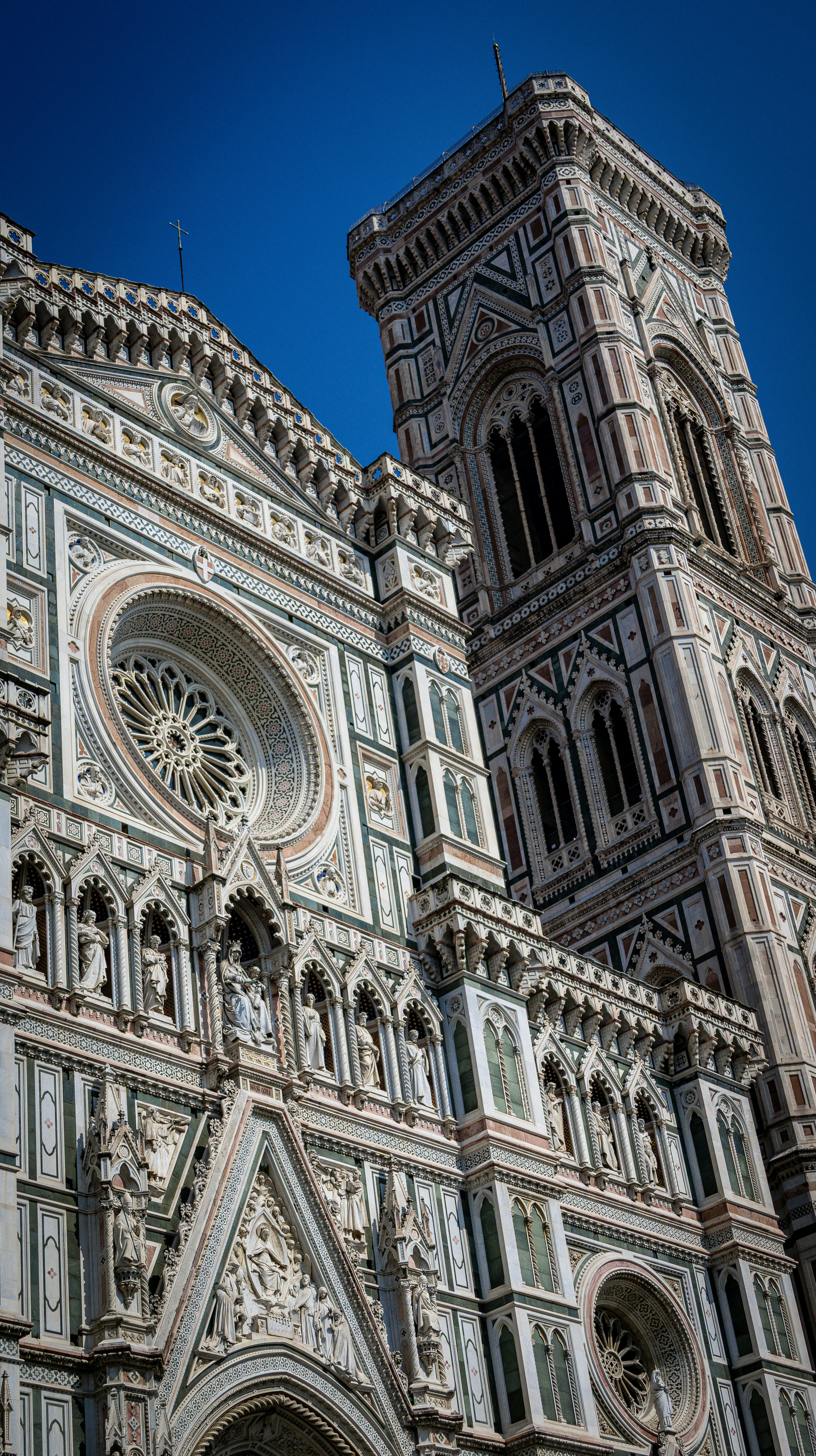 Intricate architectural details of Florence's Duomo, showcasing its ornate sculptures and colorful stonework against a clear blue sky.