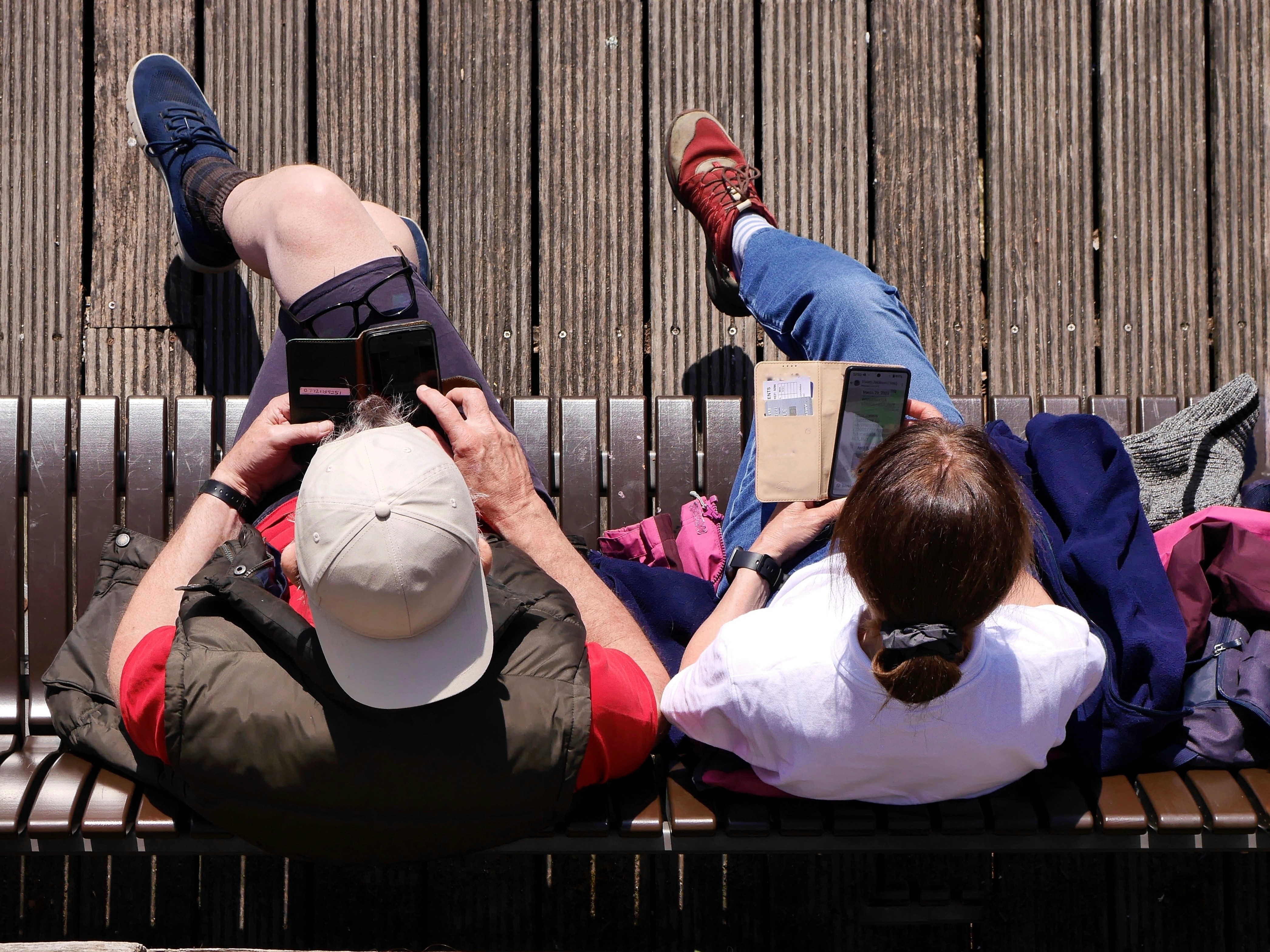 Two people sitting on a bench with phones.