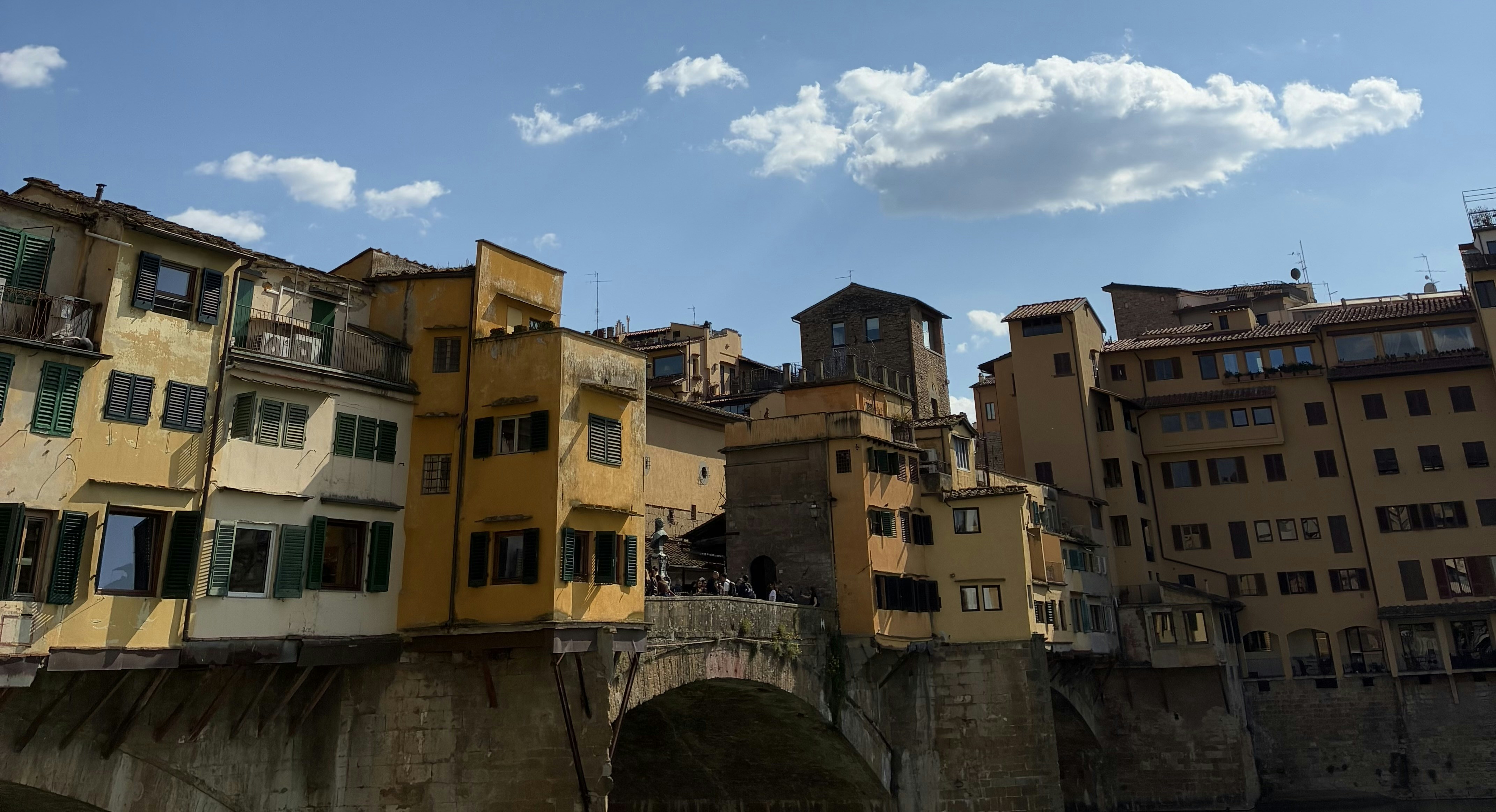Historic buildings lining the Arno River, showcasing vibrant colors and architectural charm under a partly cloudy sky.