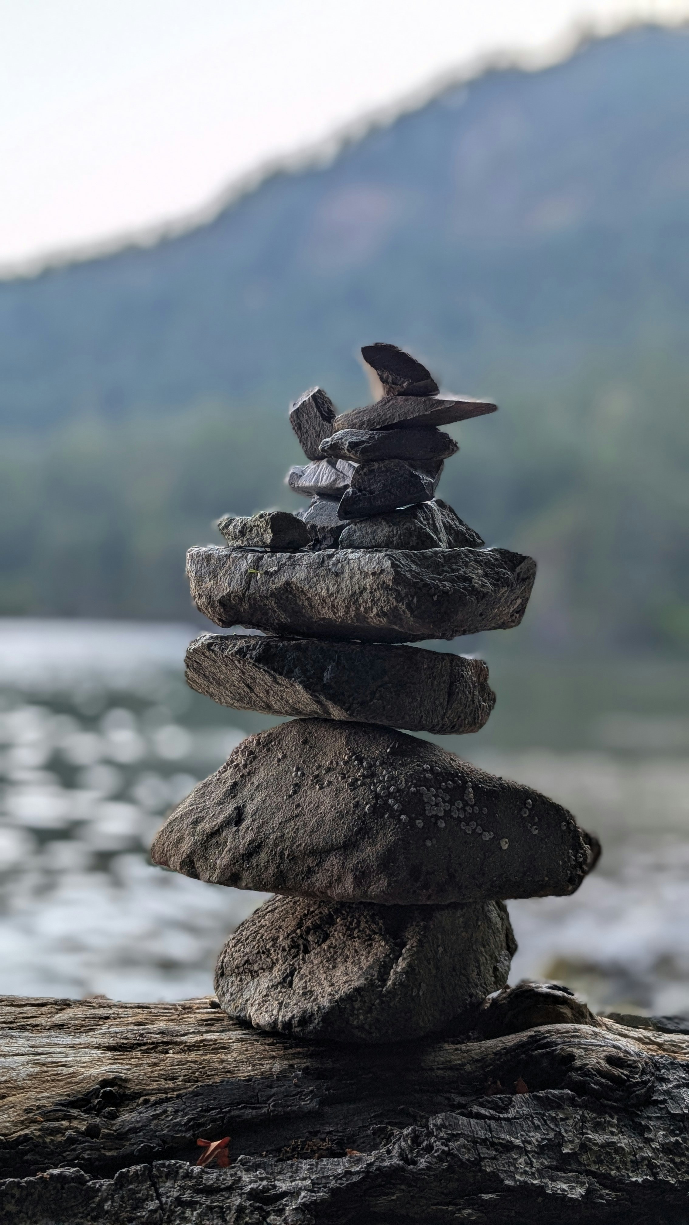 Stack of balanced stones by a lake with mountains.