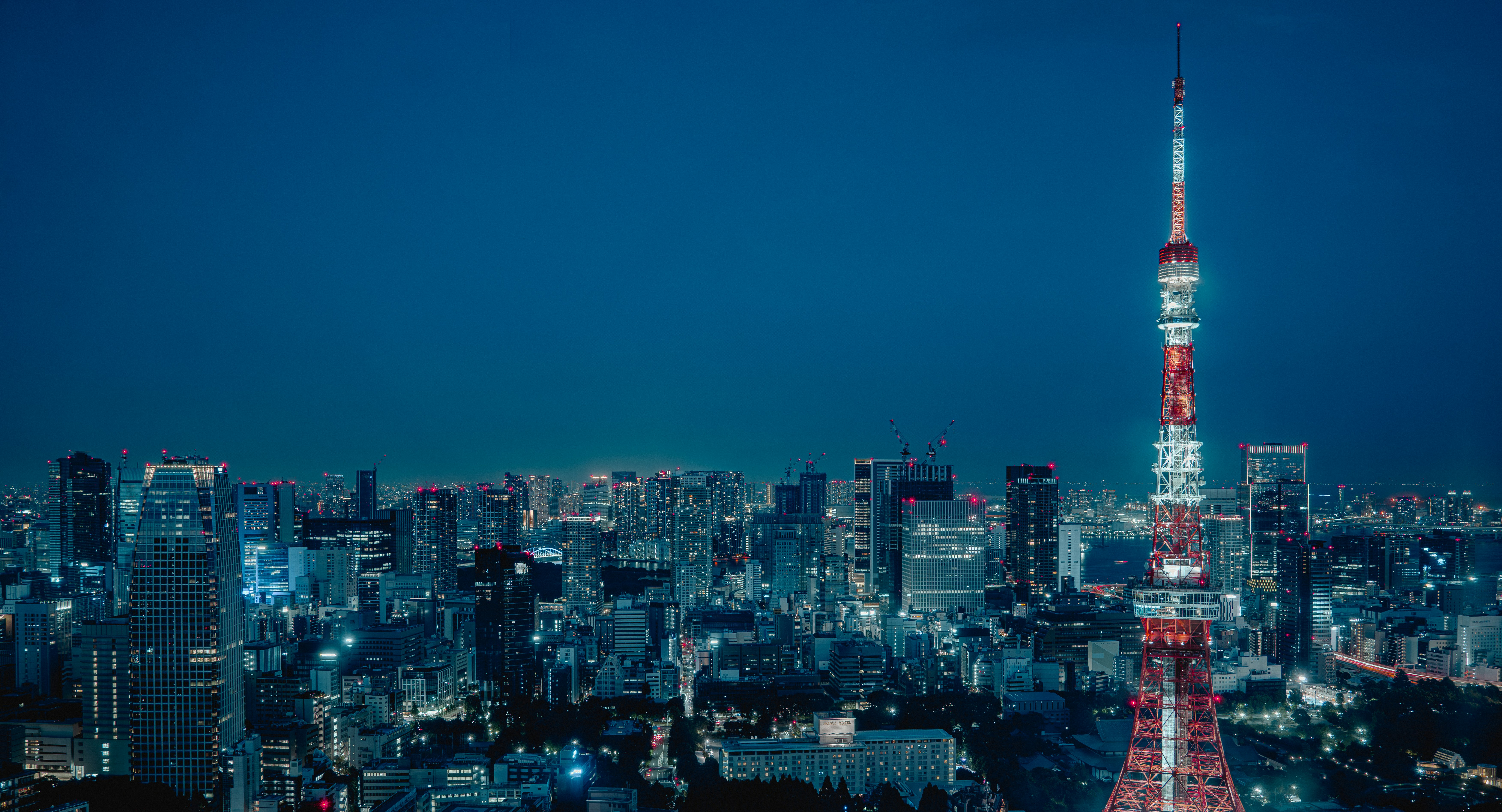 Tokyo Tower illuminated against a backdrop of a sprawling cityscape at dusk. The scene showcases the vibrant lights of the metropolis.
