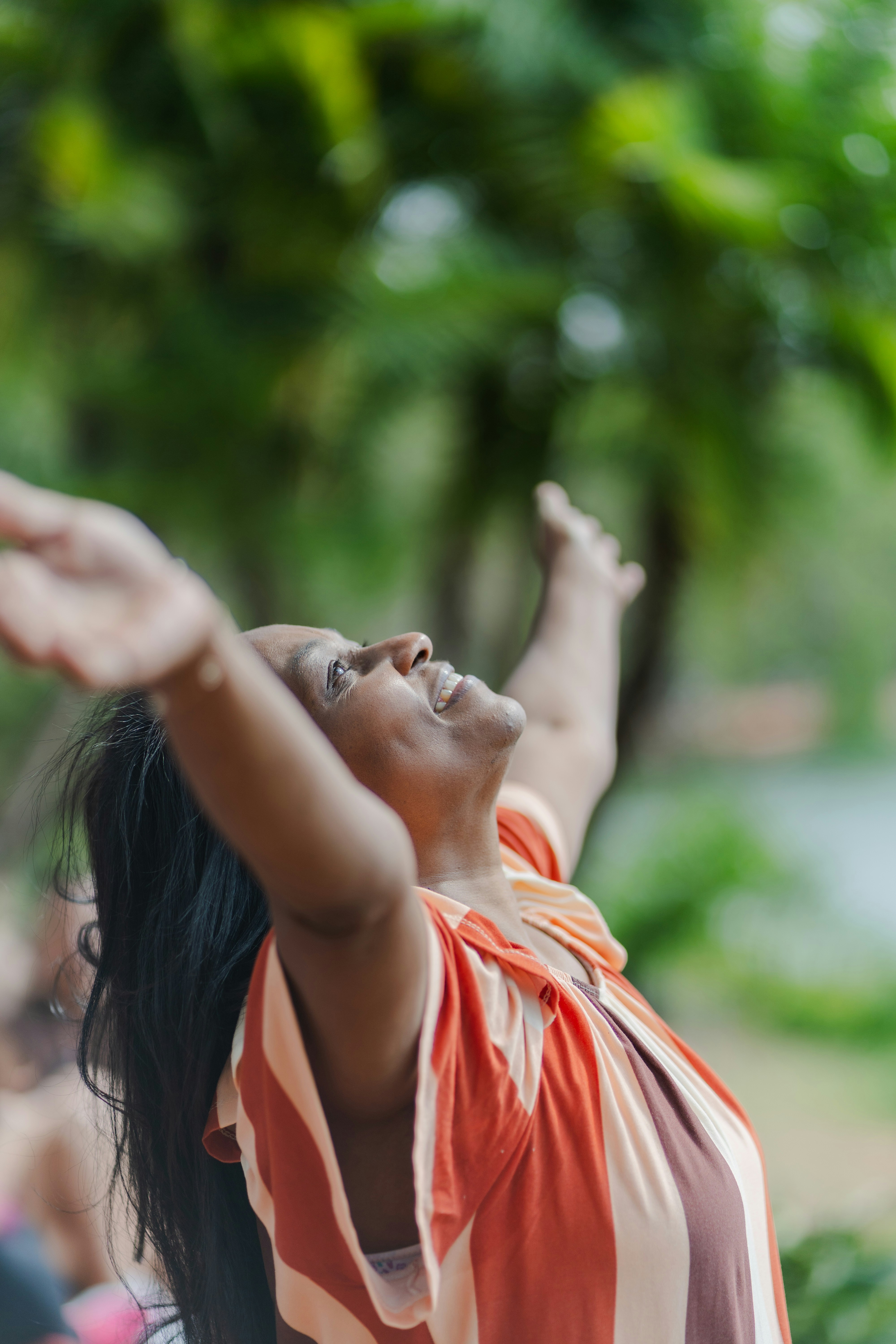 Woman with outstretched arms, expressing joy and liberation against a lush, green backdrop. Natural light enhances the serene atmosphere.