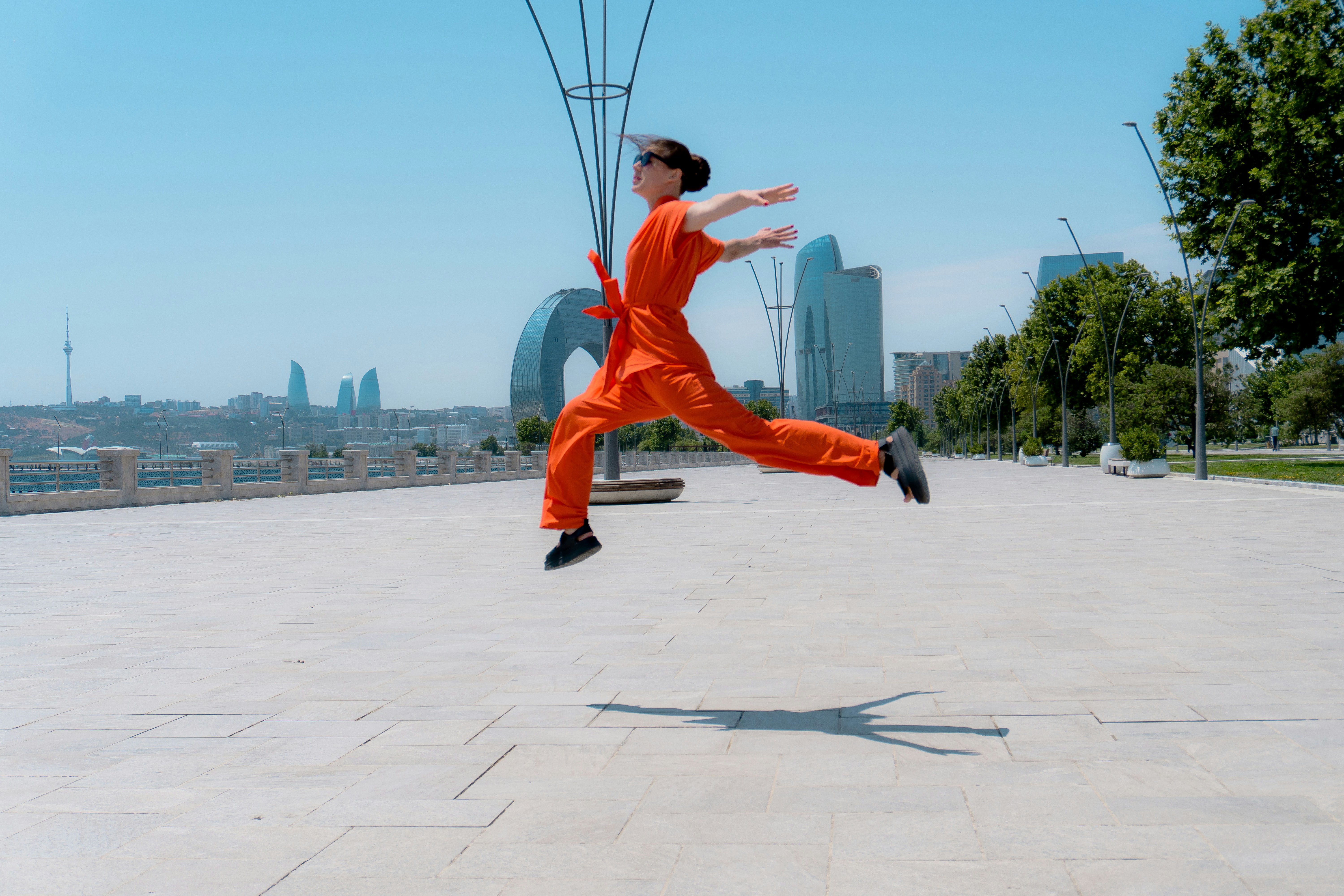 Young woman wearing orange dress doing sports | Woman in orange jumpsuit jumping outdoors with city skyline background