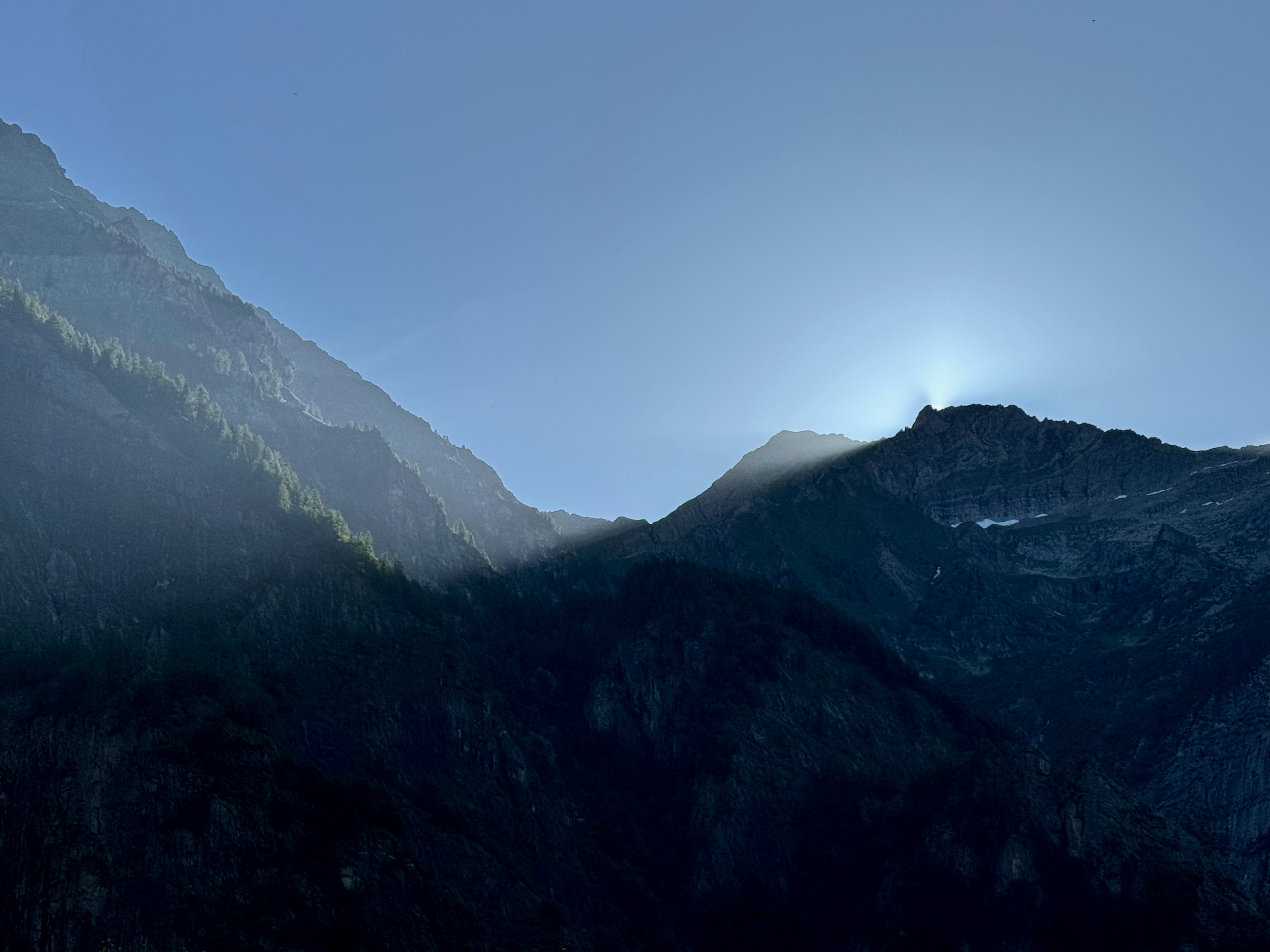 Sun peeking over a dark mountain ridge.