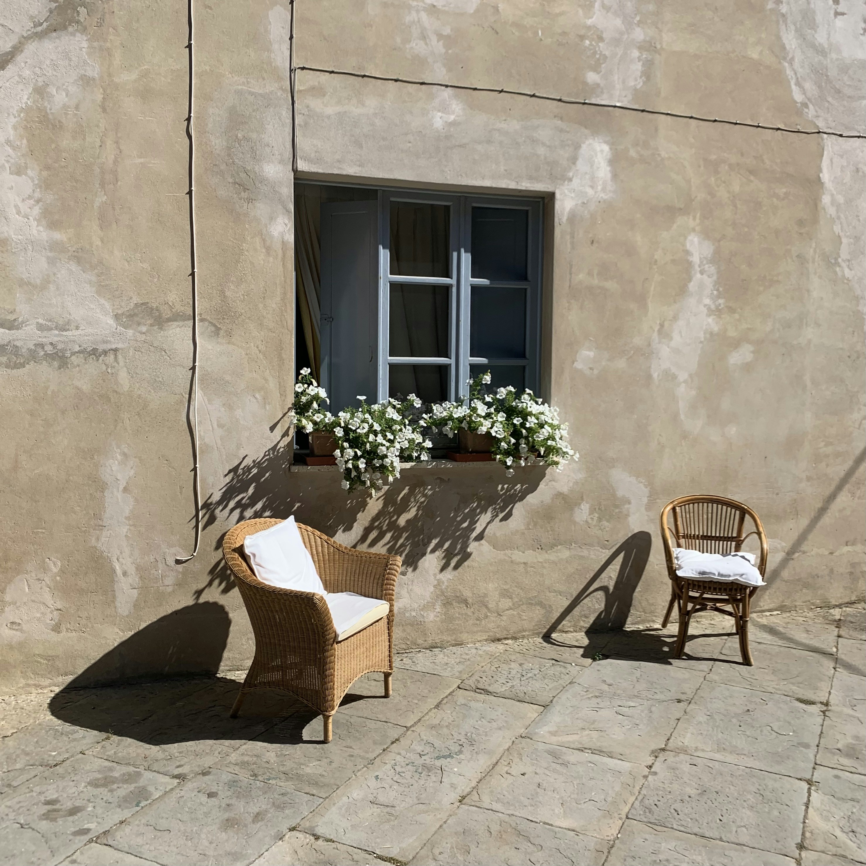 Charming outdoor seating beside a flower-adorned window on a textured wall, inviting relaxation. The scene captures the essence of serene outdoor living.