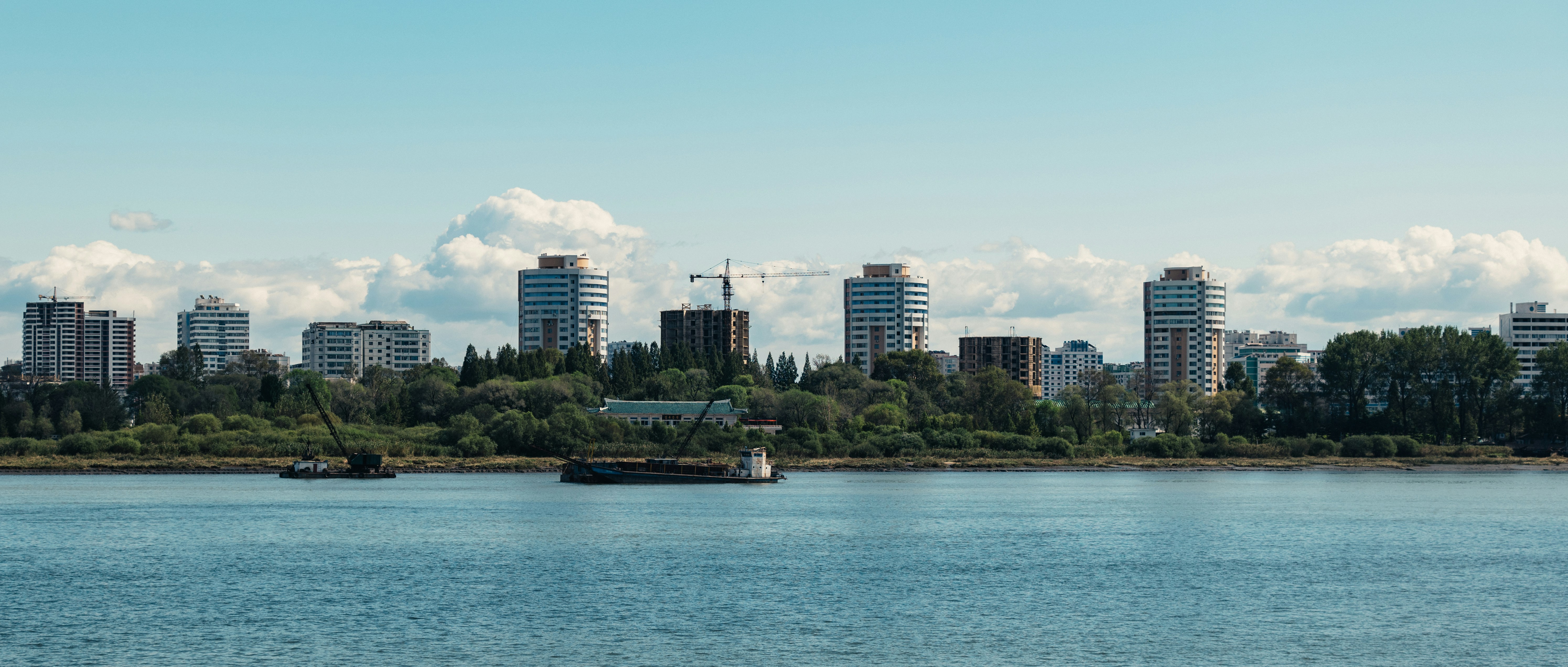 City skyline with buildings and barges on water.
