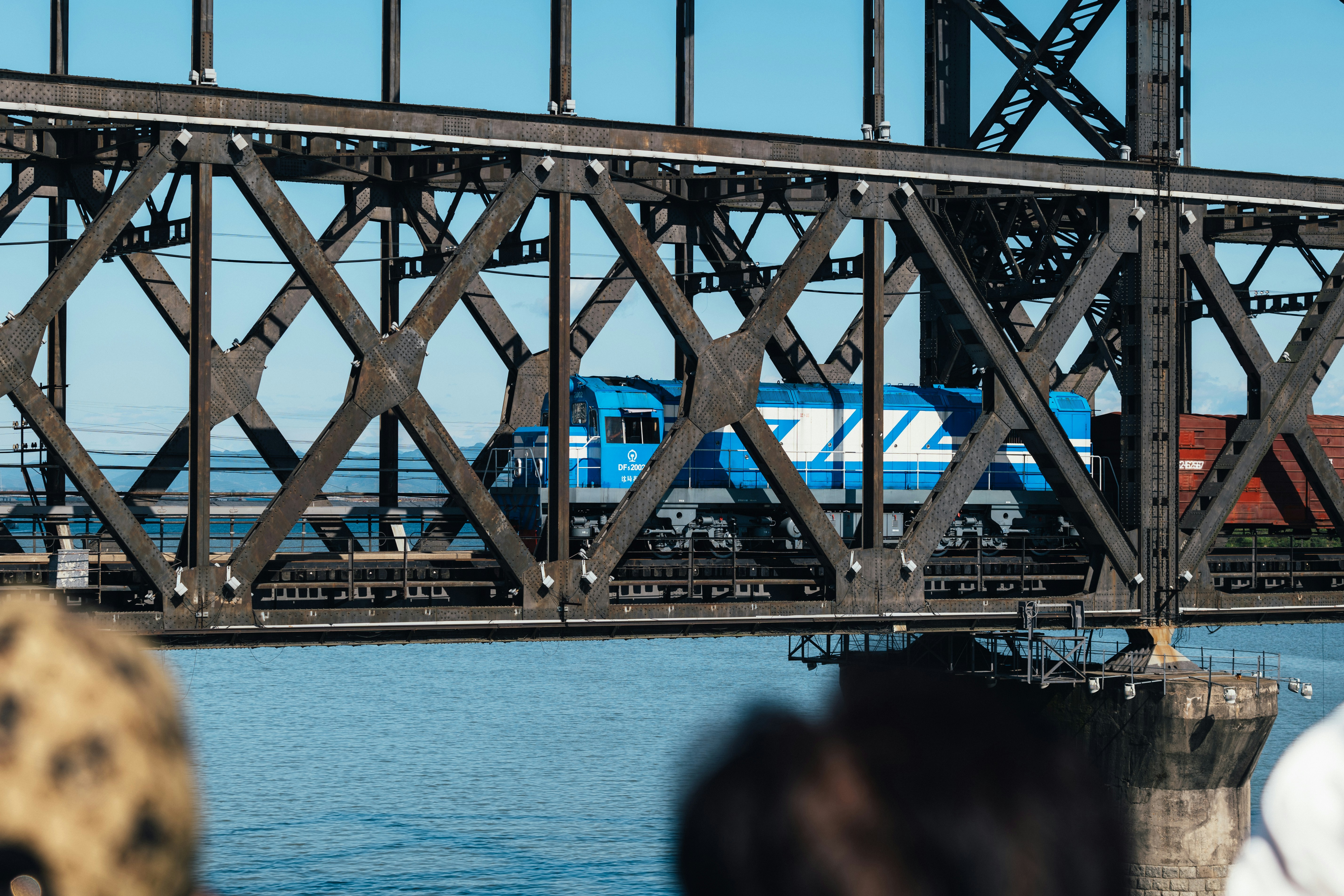 Blue Locomotive Crossing a Lattice Bridge Over Quiet Harbor