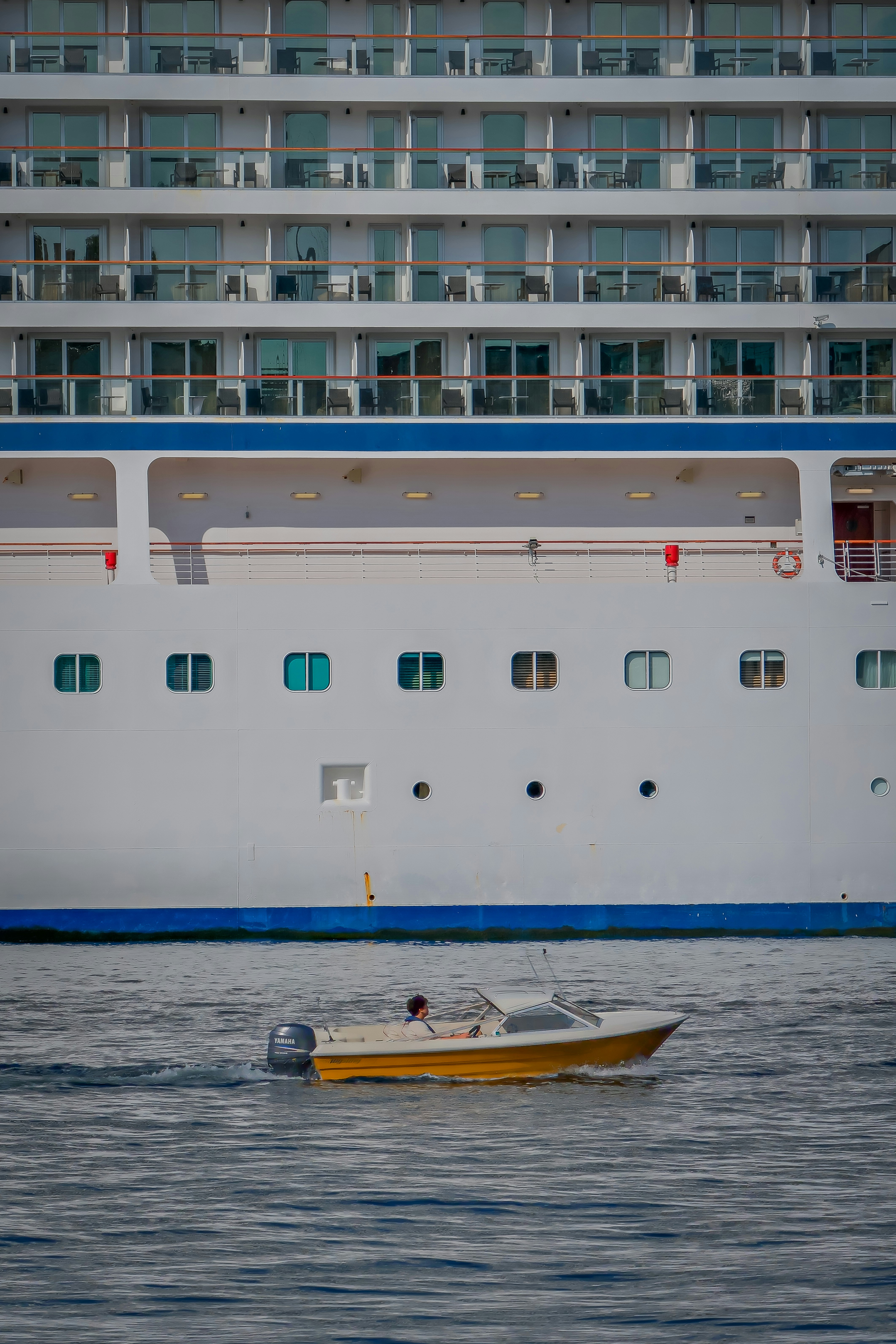 A bright yellow motorboat navigates across calm waters in front of a towering white cruise ship. | A small boat sails past a large cruise ship.