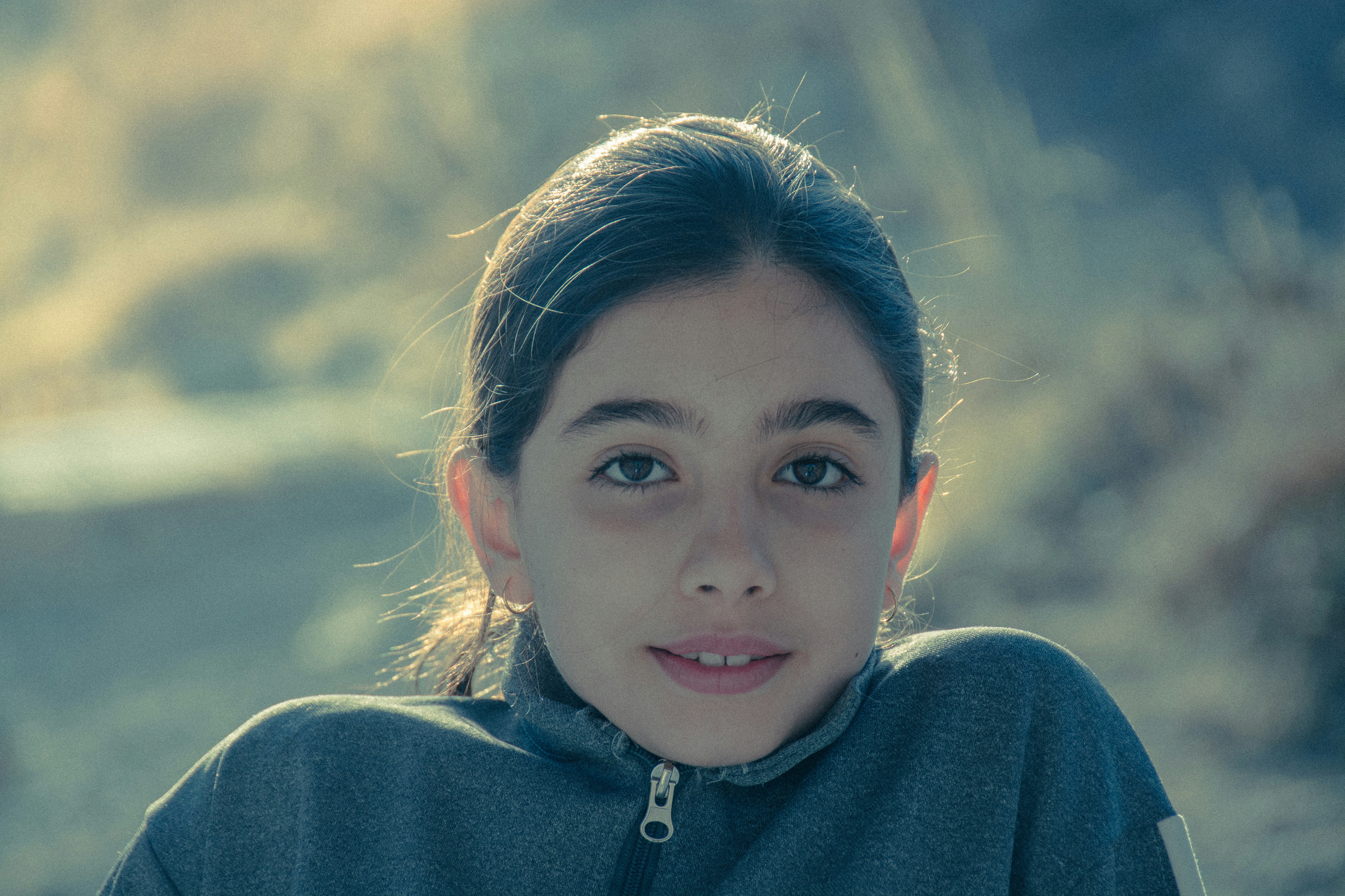 Young girl with dark hair smiles gently outdoors.