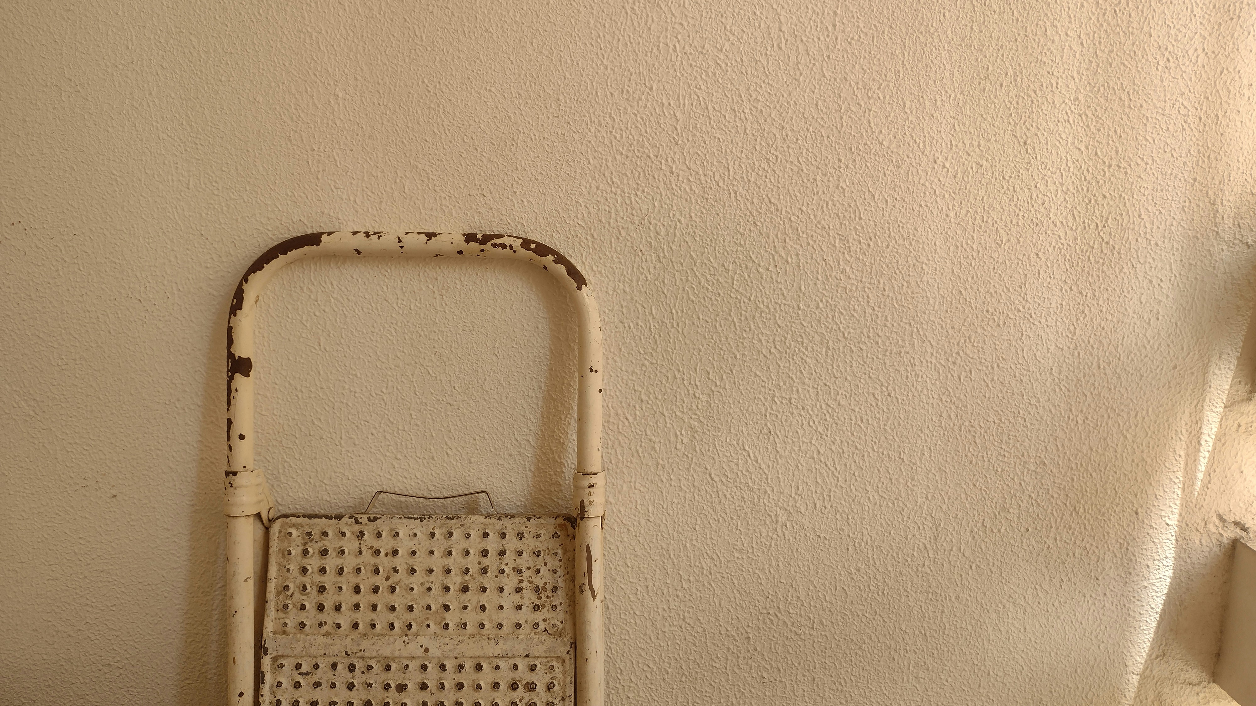 A white metal step stool against a textured wall.