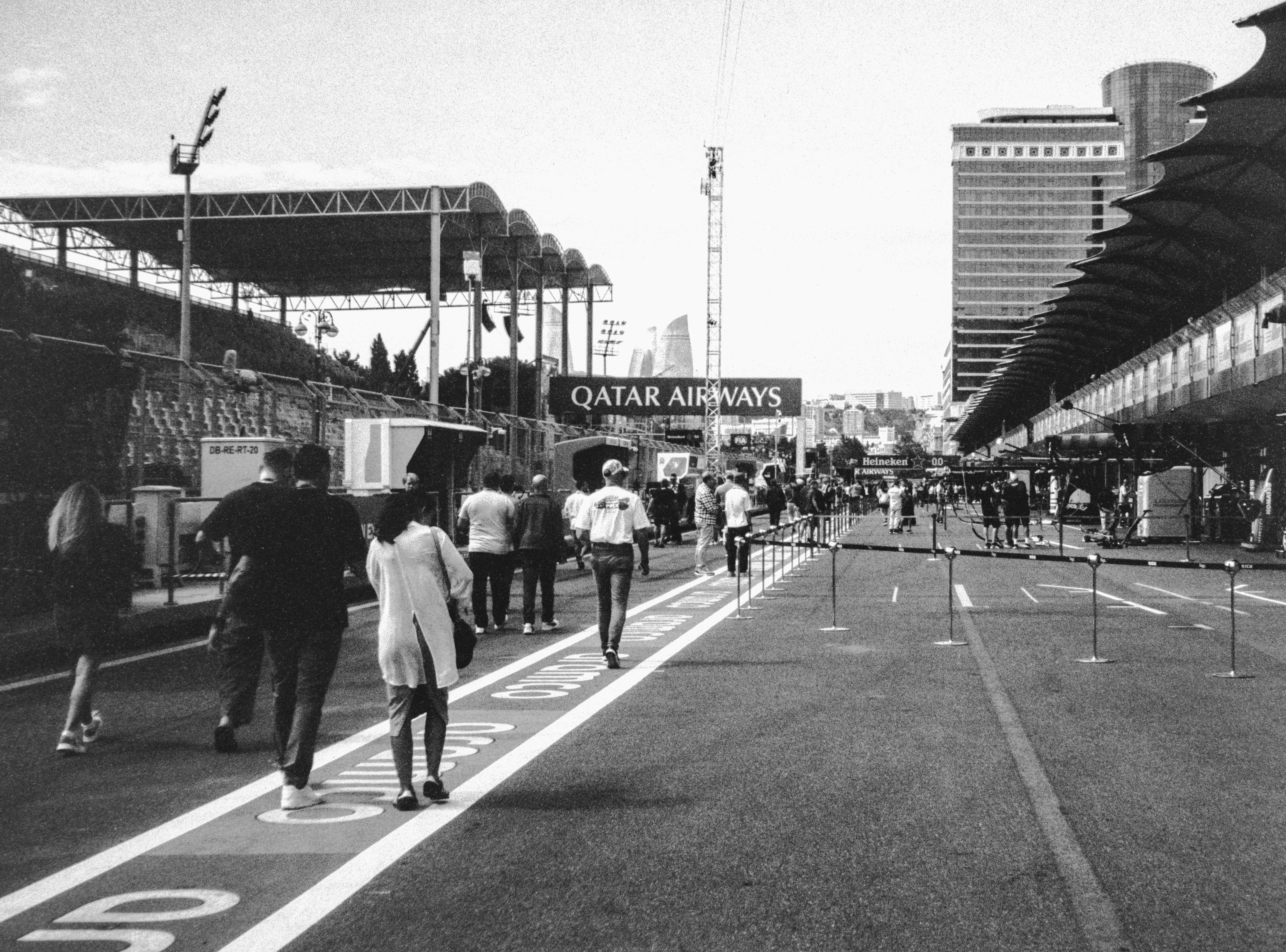 Crowd of spectators walking along the pit lane of a racetrack, with the Qatar Airways banner prominently displayed in the background.