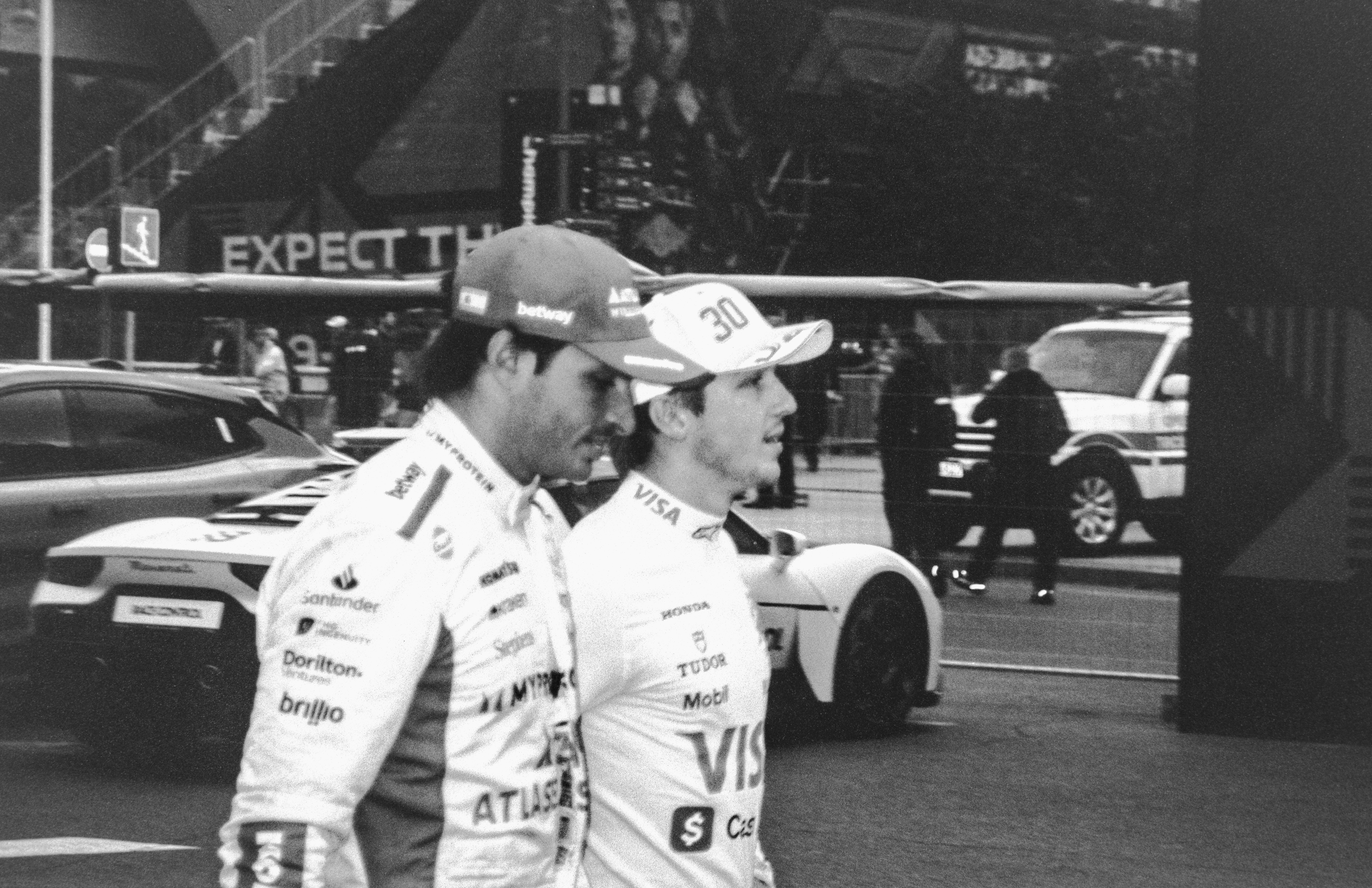 Two men in racing suits walk side-by-side.