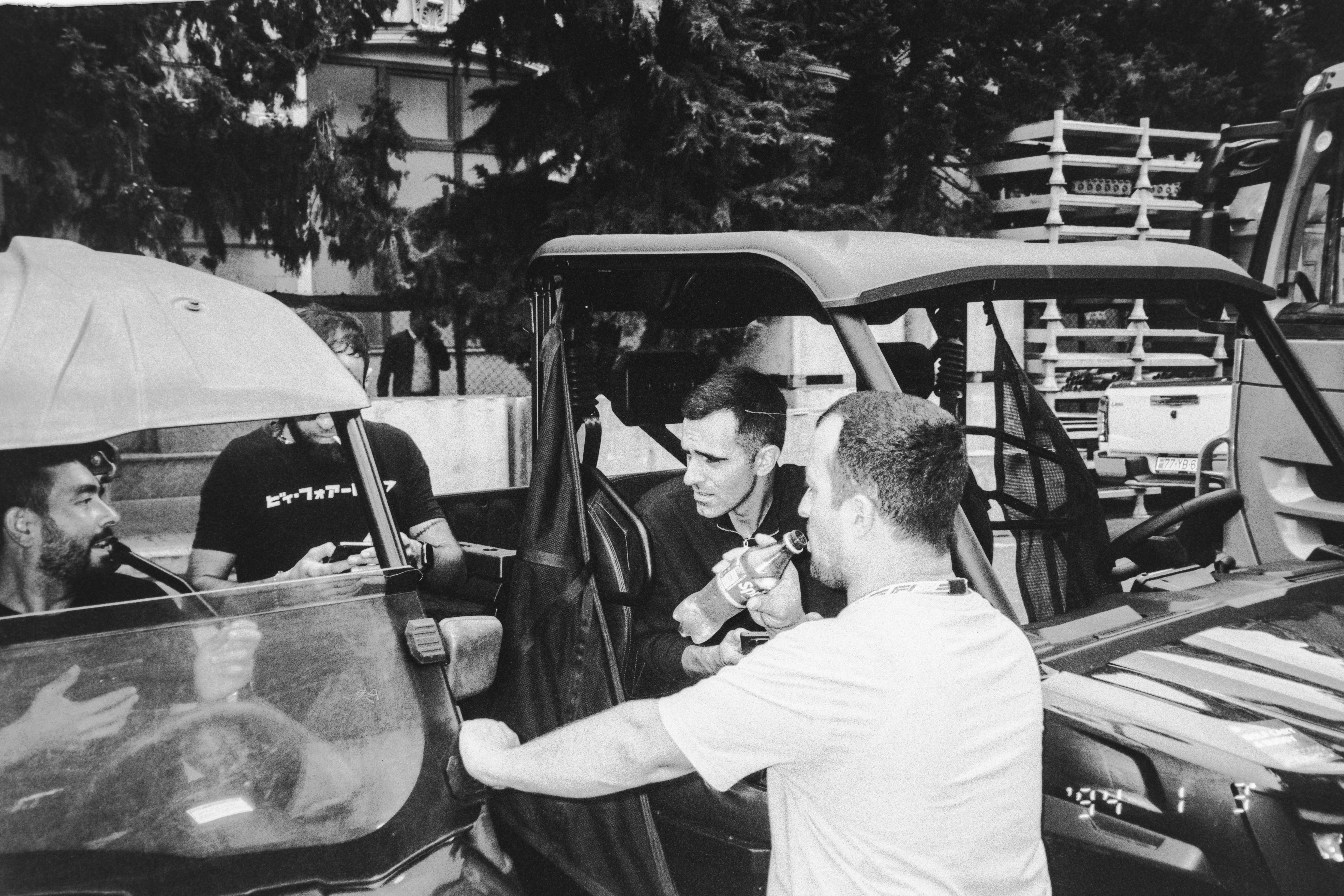 Men gather around a car door in black and white