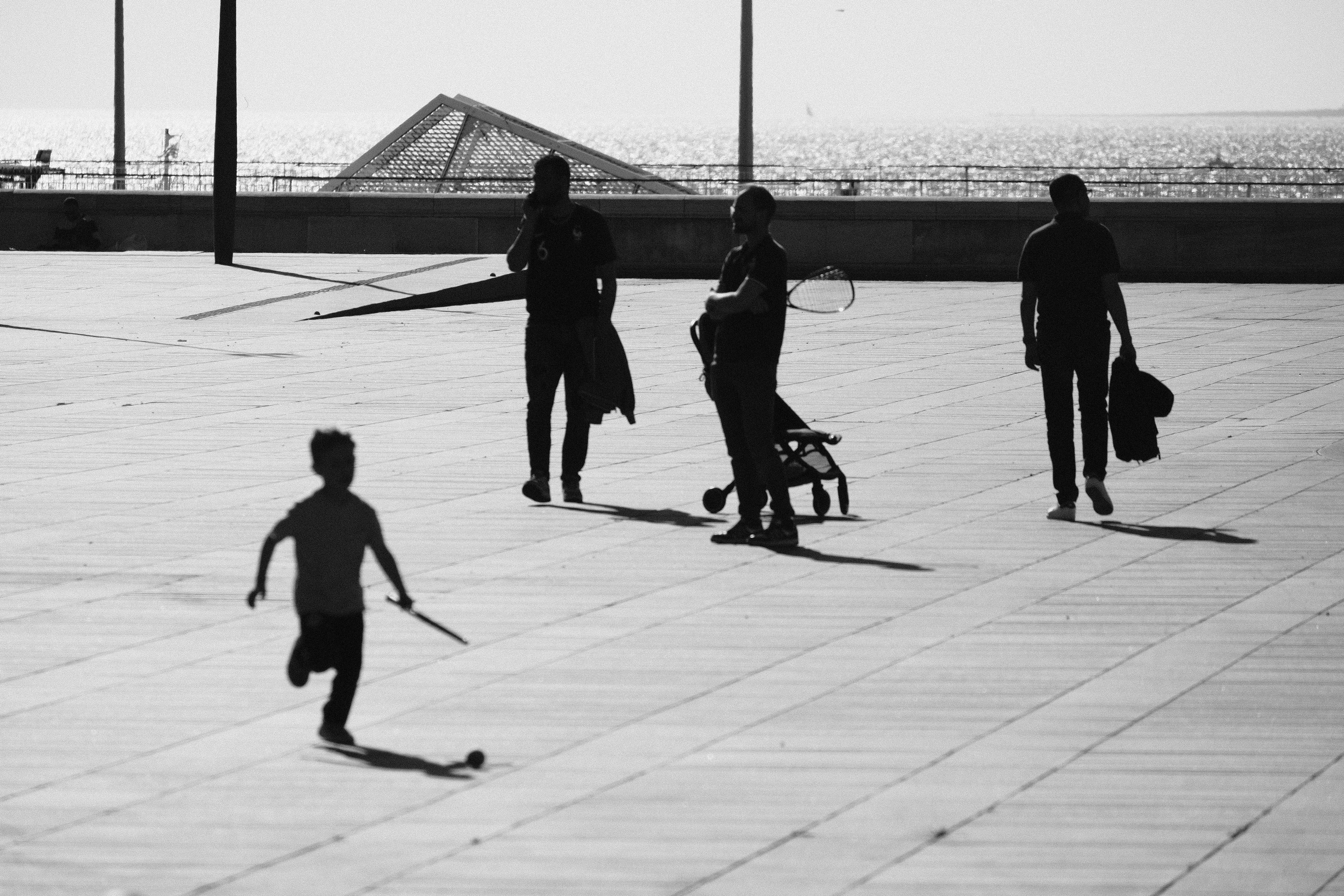 Silhouettes of people walking on a paved plaza