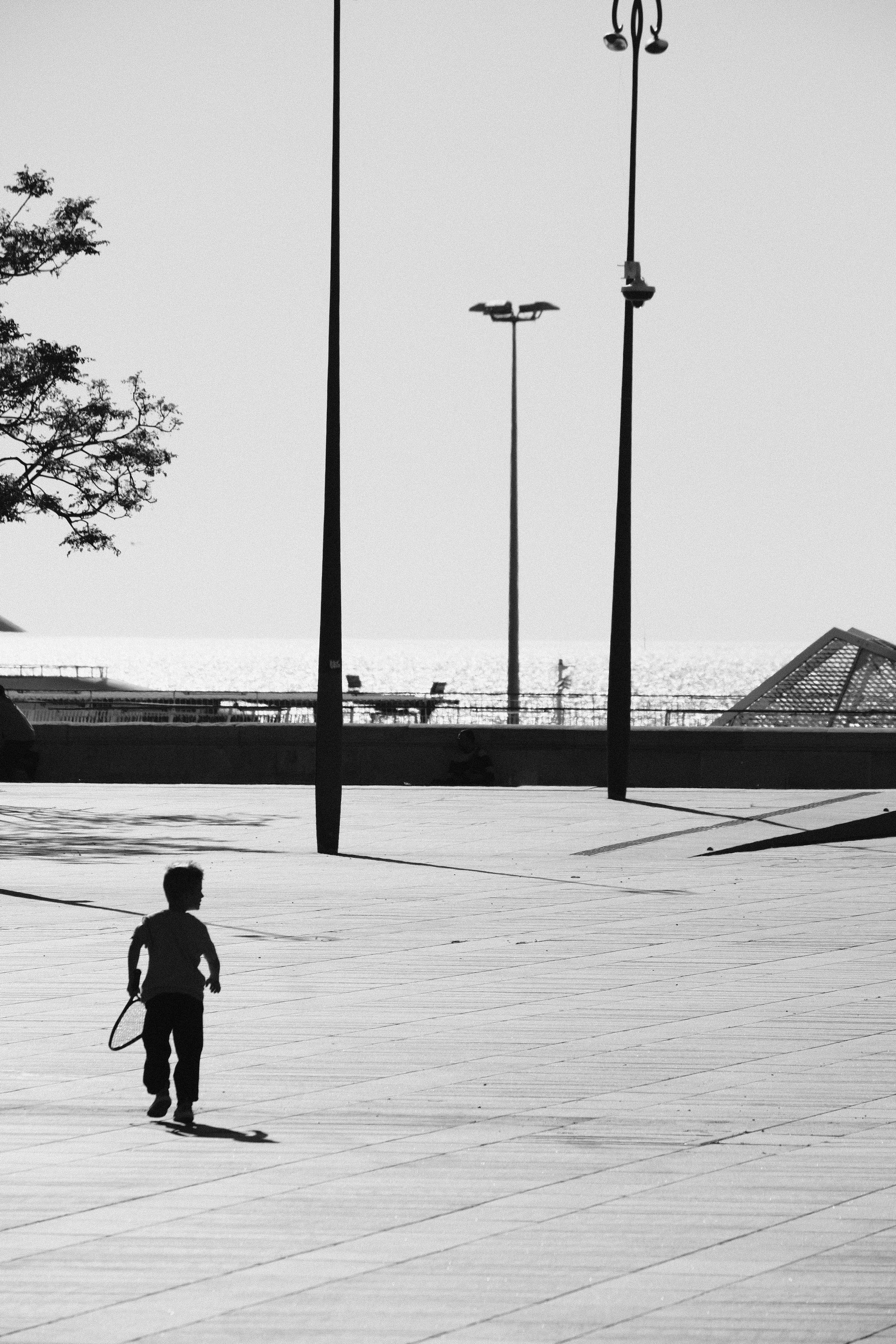 Boy with hoop walks in sunny plaza near ocean