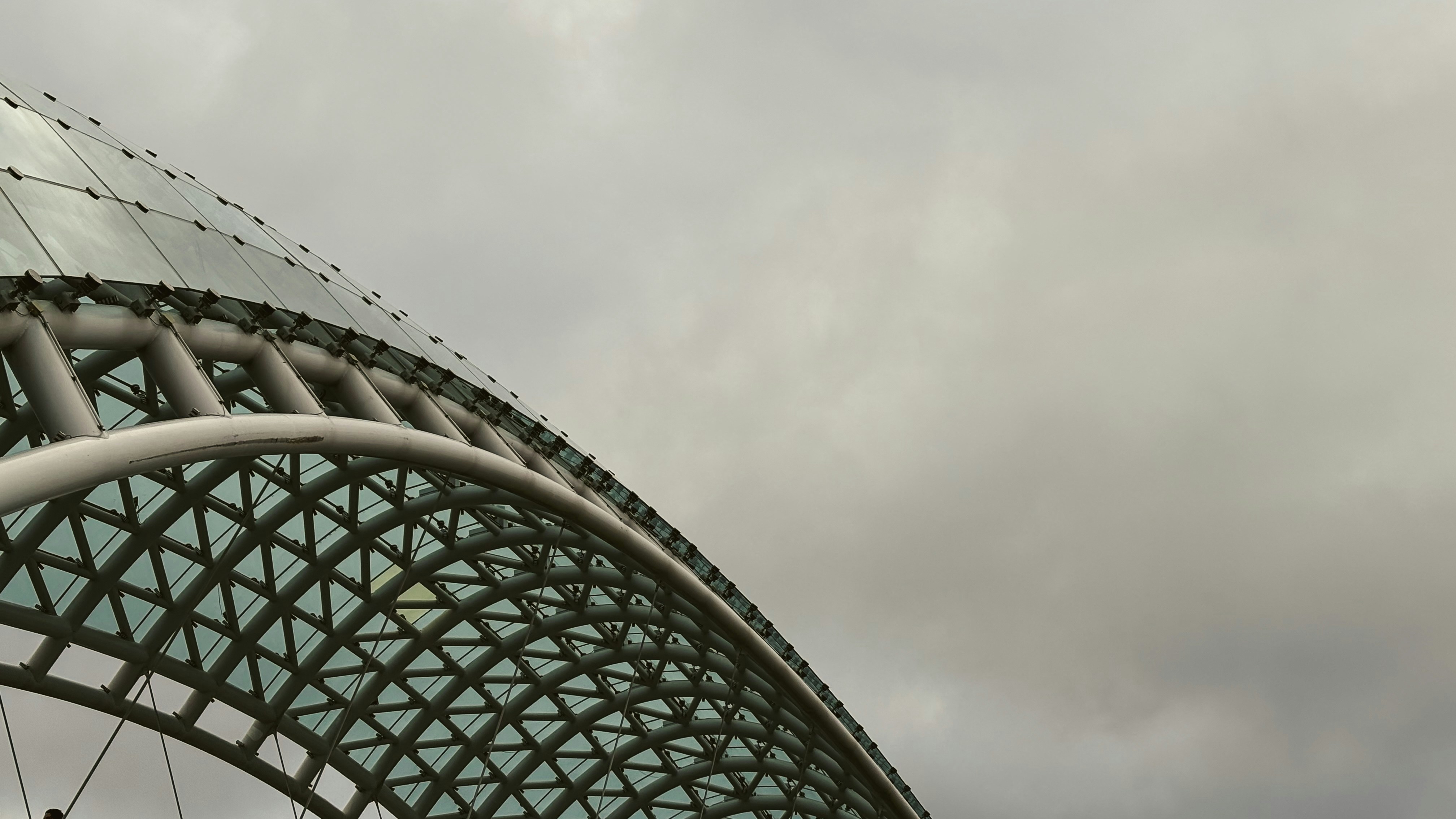 A modern architectural structure featuring a sweeping glass and metal canopy against a cloudy sky.