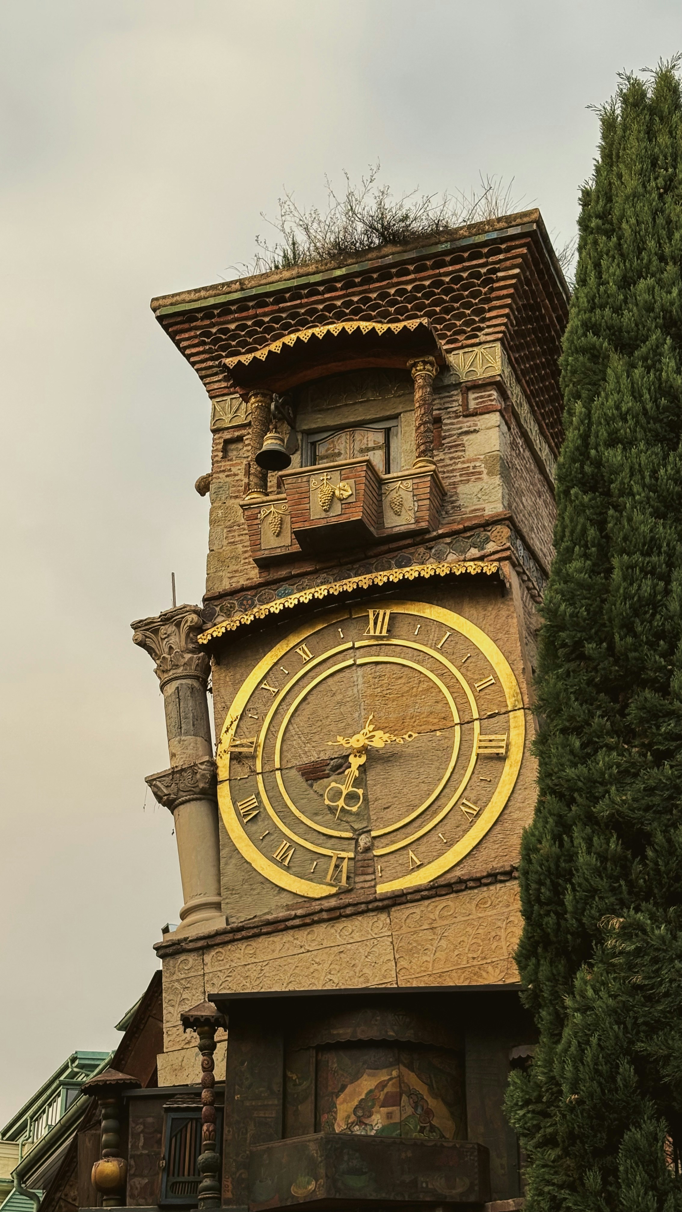 The whimsical leaning clock tower of Tbilisi, with its ornate golden clock face and playful architectural details, stands as a fairytale-like landmark in the city’s old town. | Ornate clock tower with roman numerals and golden hands.