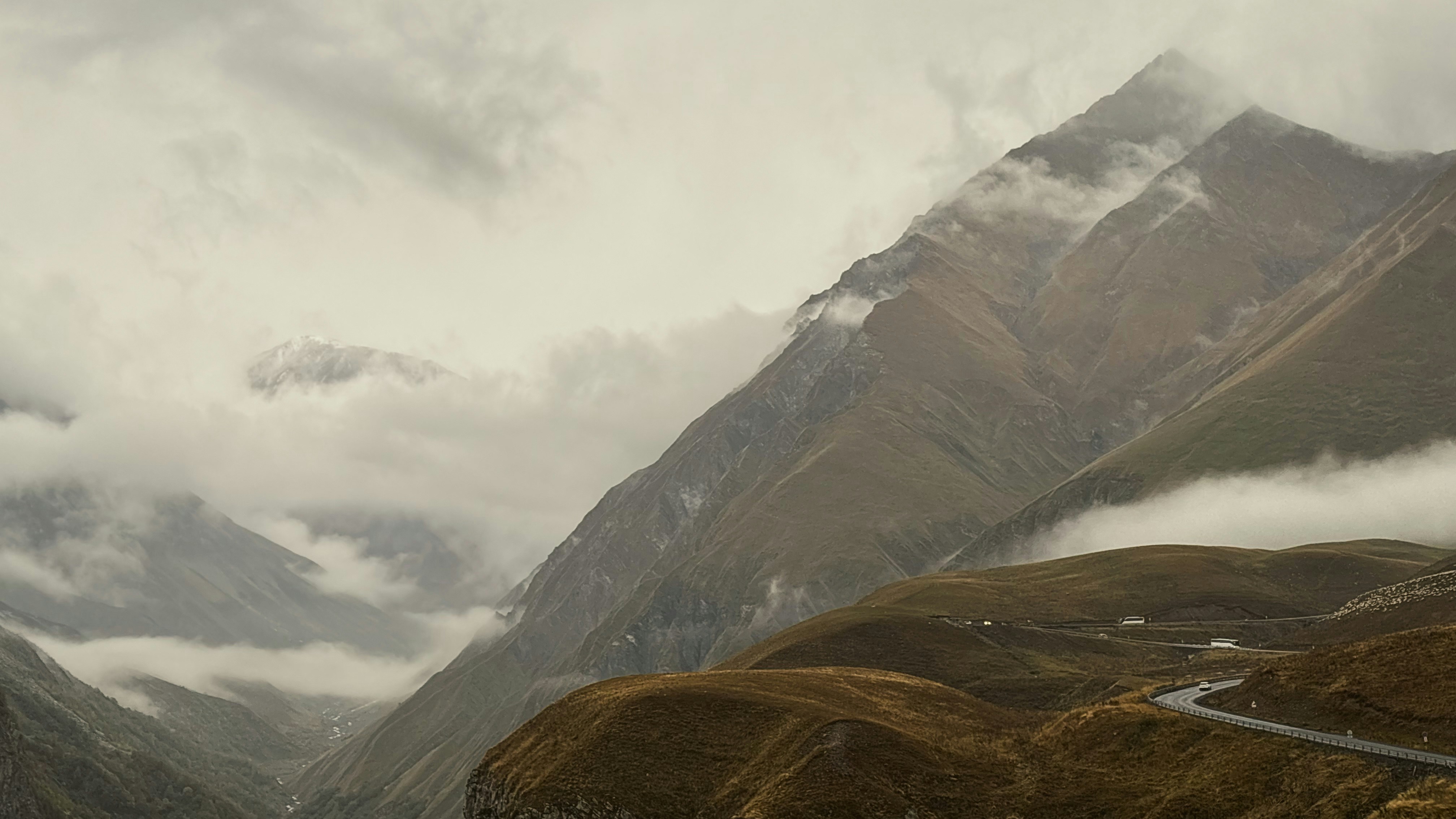 Clouds envelop rugged mountain peaks, revealing winding roads that traverse the dramatic landscape.