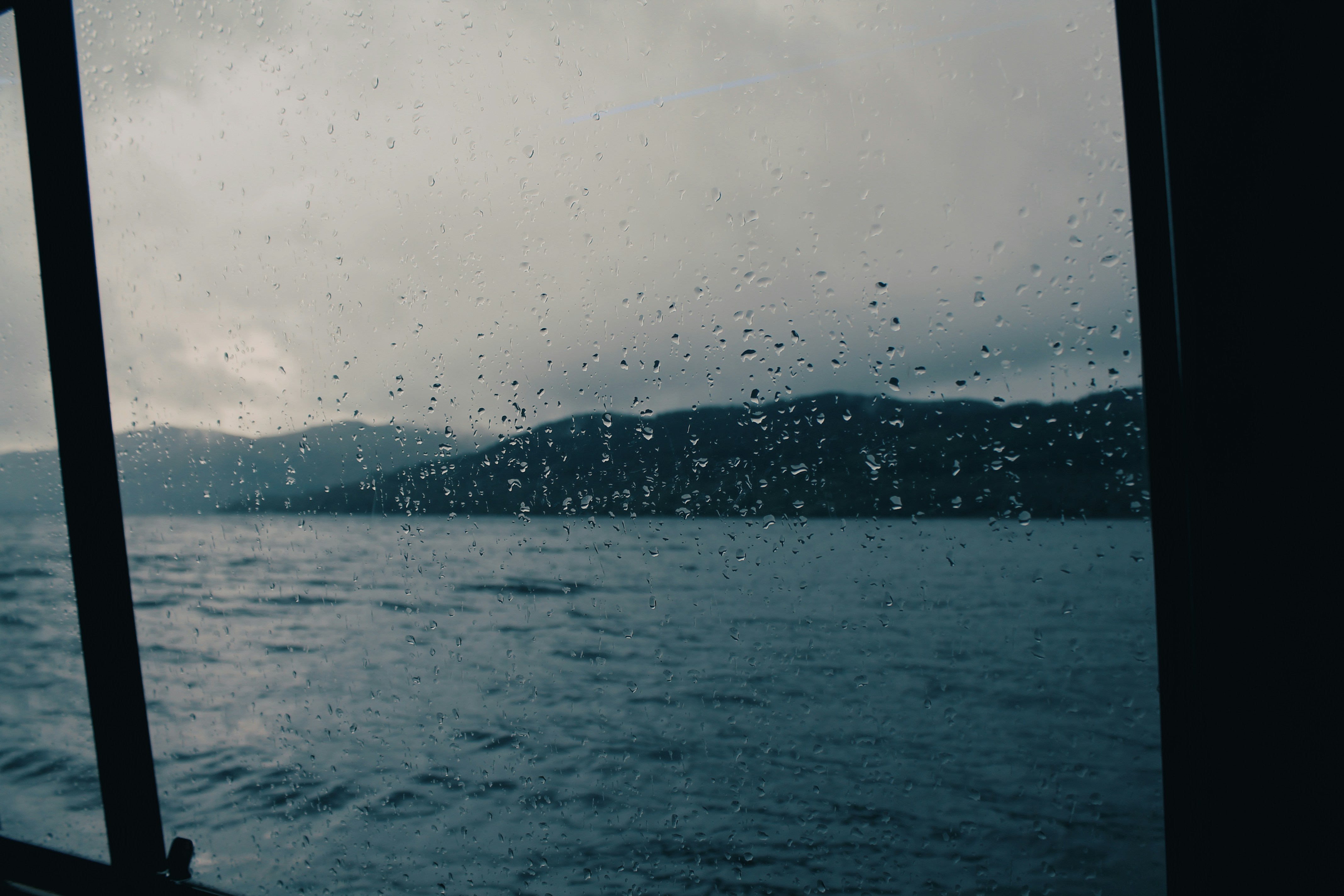 Raindrops on window overlooking a dark, choppy sea.