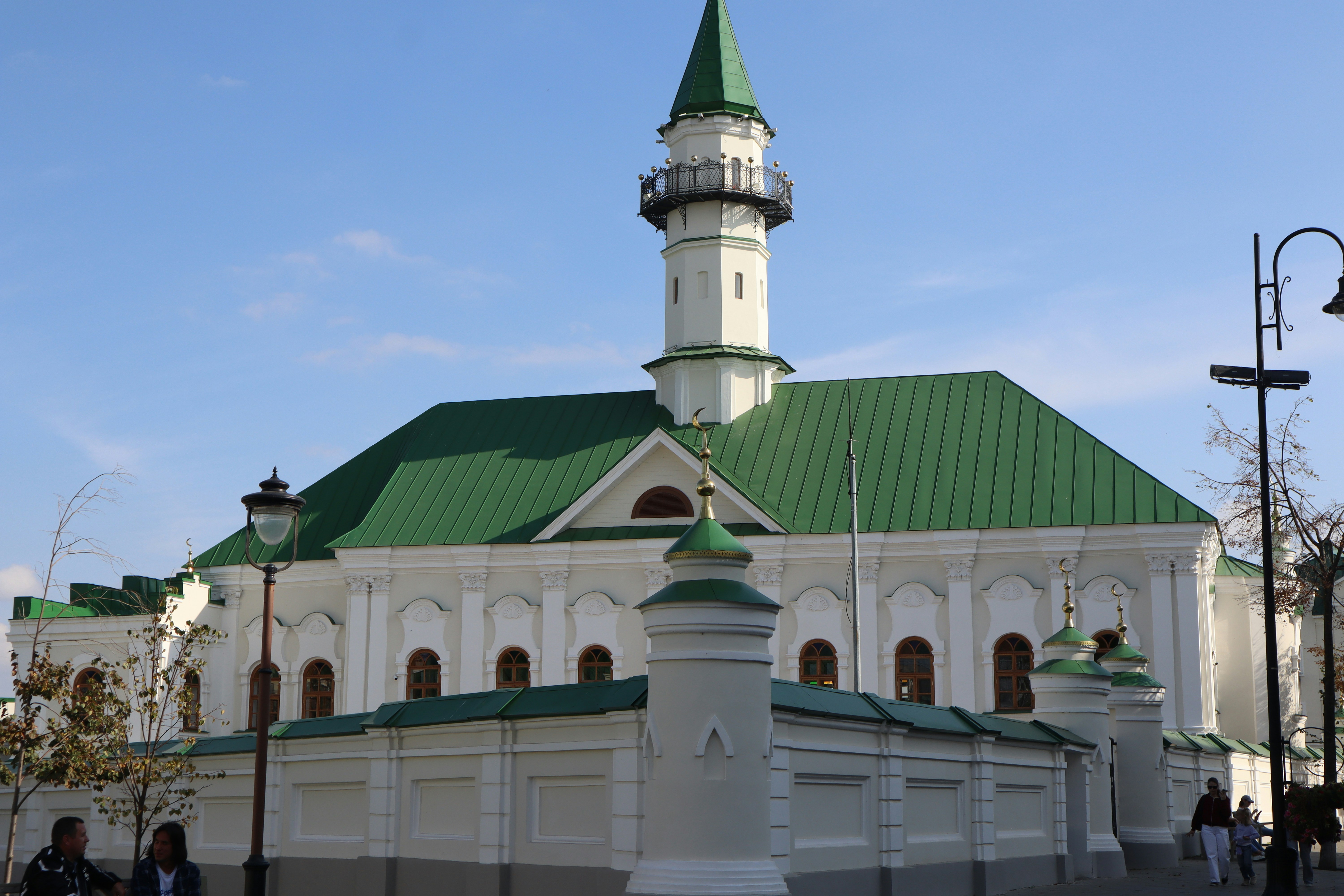 A striking mosque with a green roof and white facade, framed by trees and lampposts in a serene urban setting.