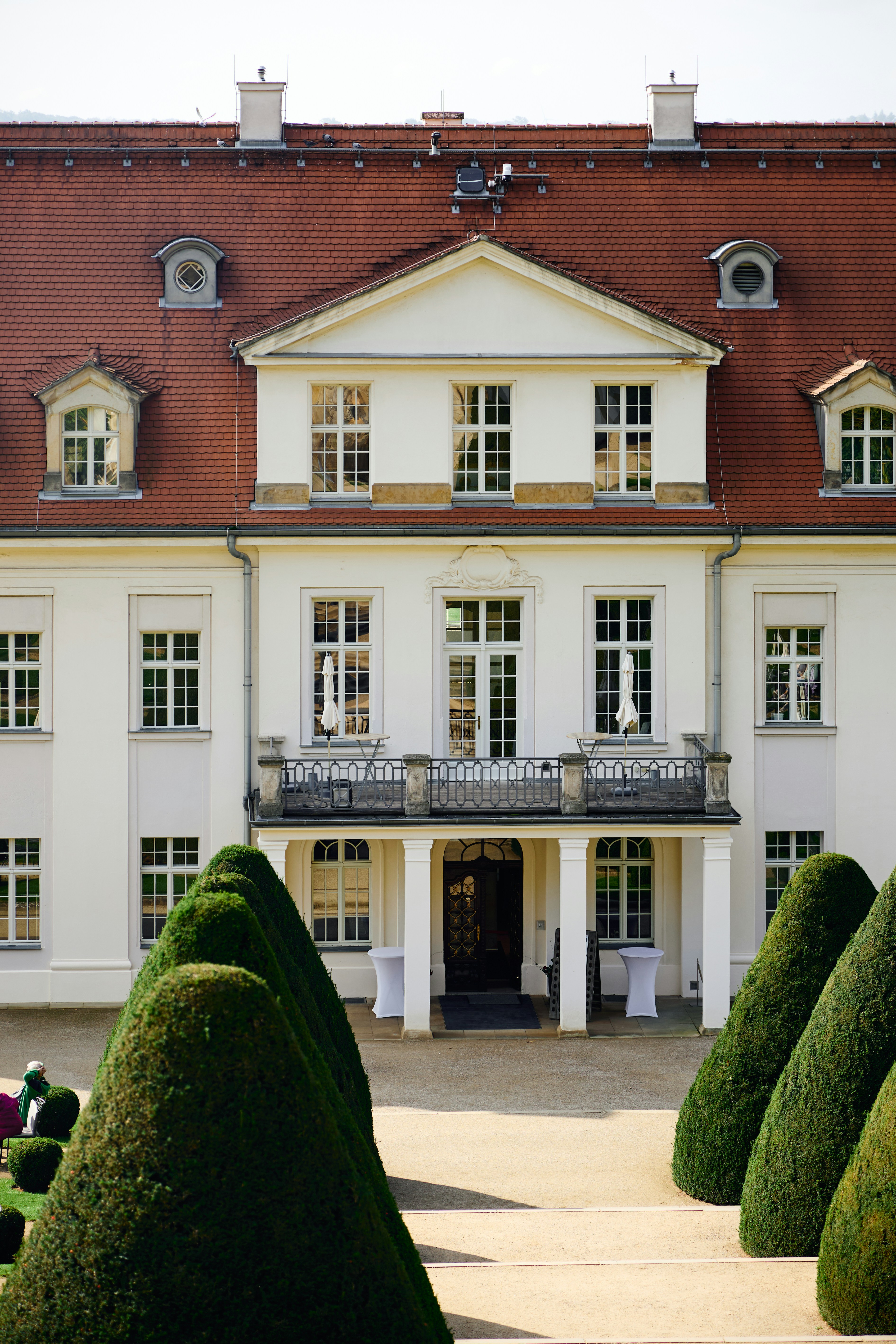 Grand white building with red roof and manicured hedges.