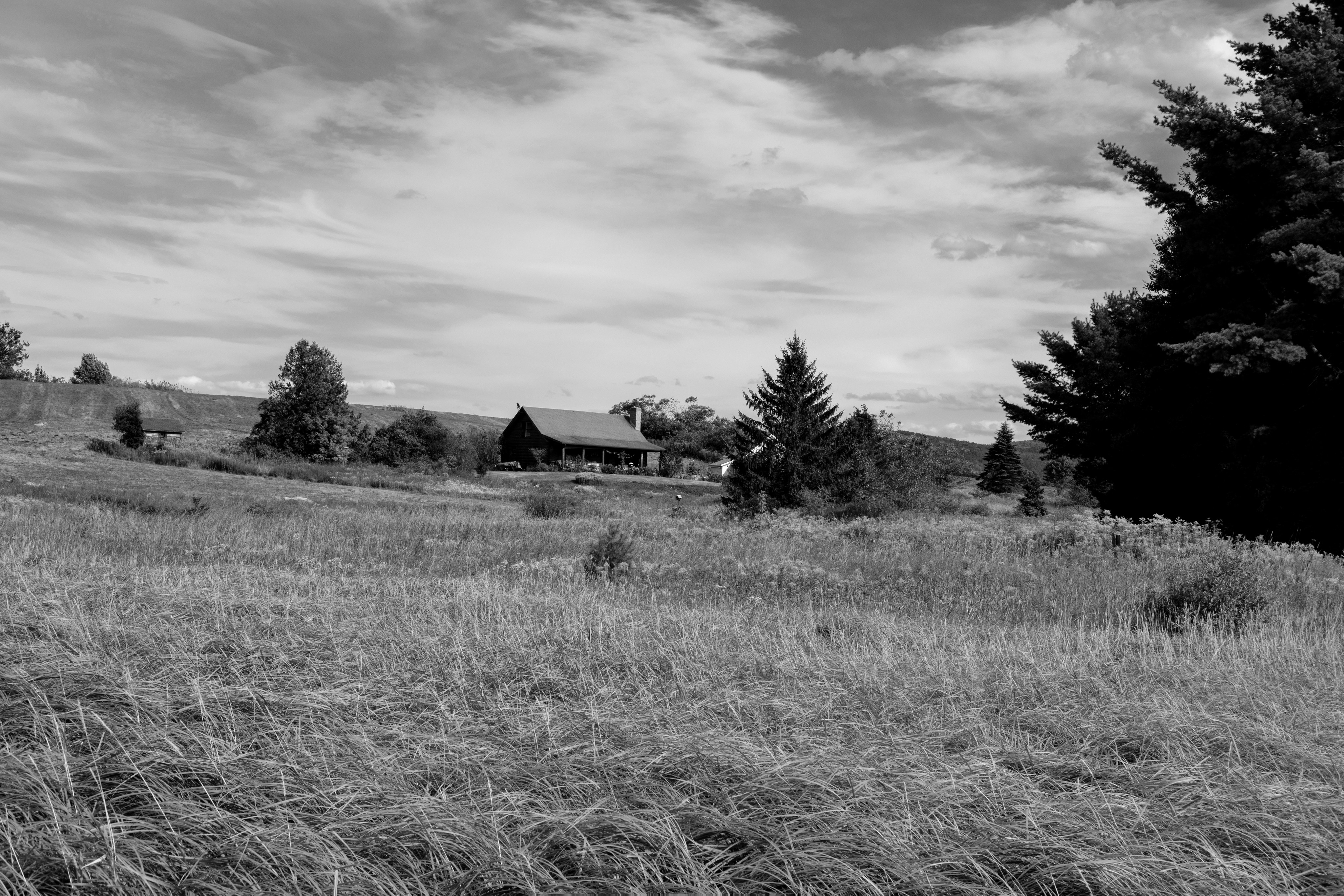 A rustic cabin sits on a grassy hill under clouds.